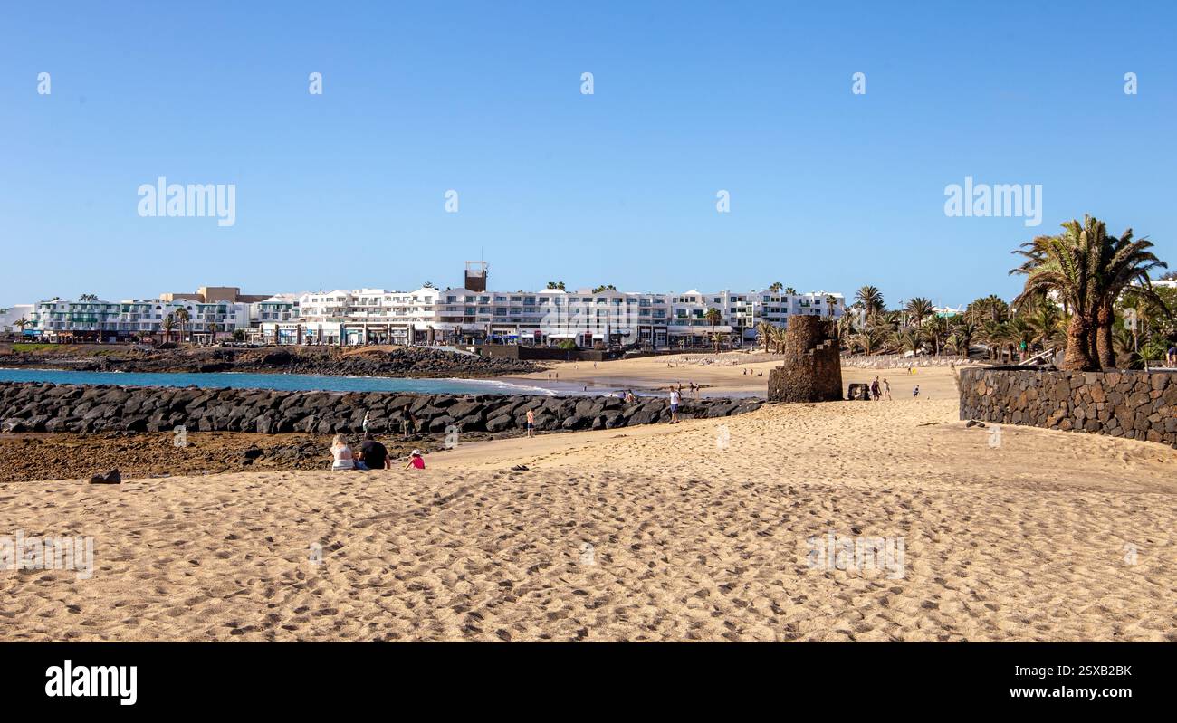 Sunny sandy beach view with people relaxing and a coastal town in the ...