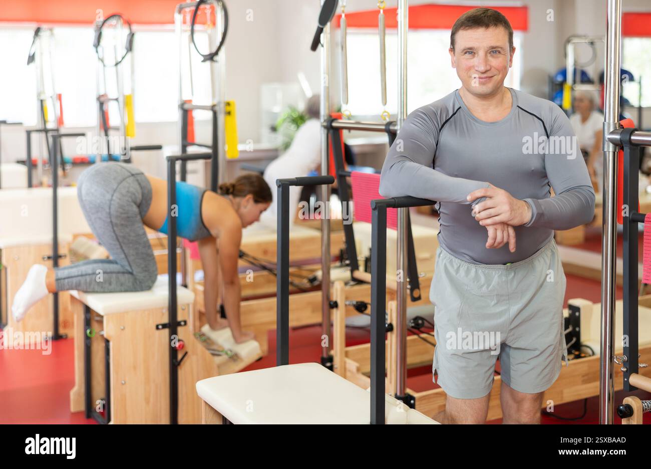 Positive man coach stands in large gym against background of Pilates ...