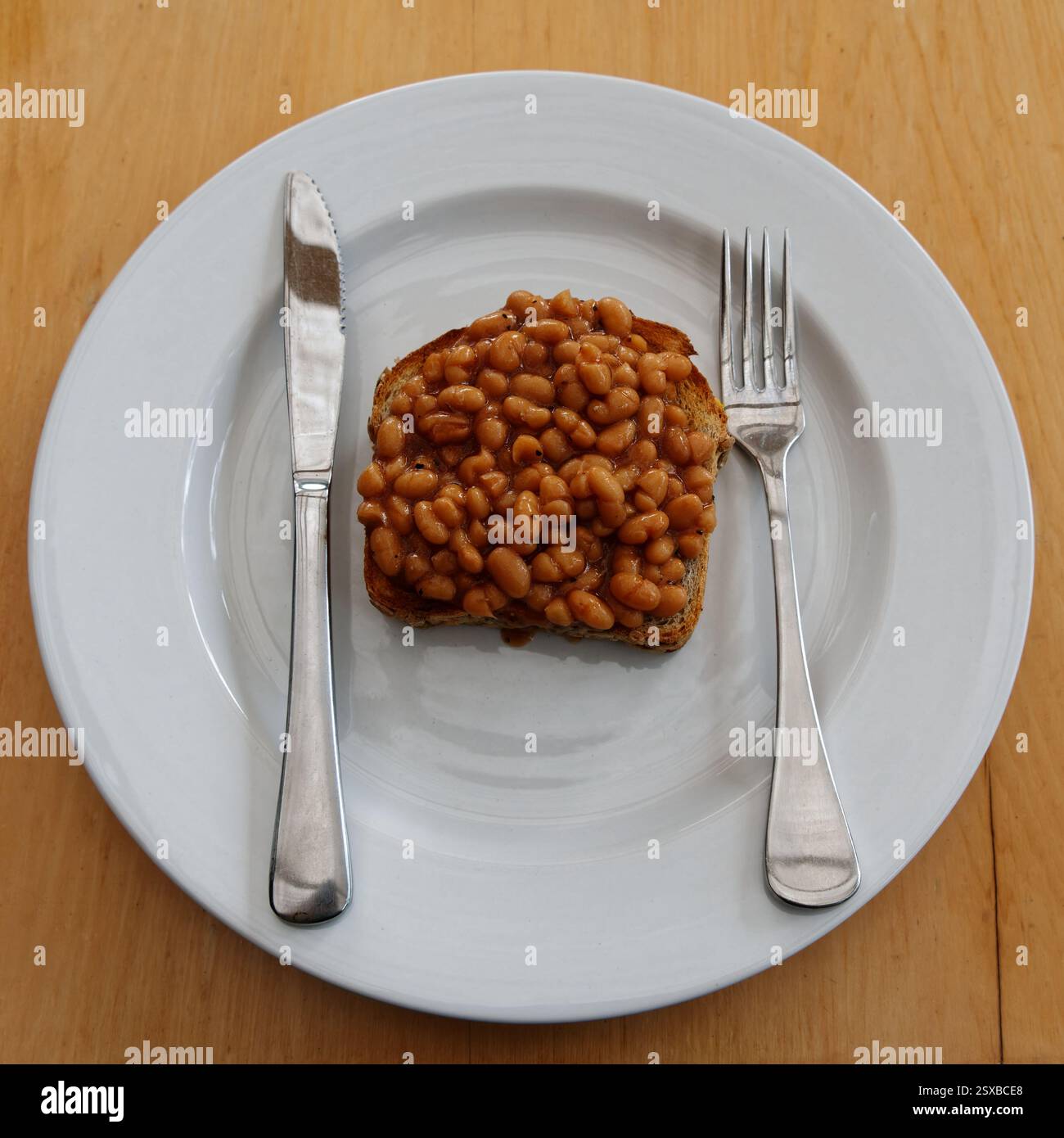 Baked beans on toast ready to be eaten. They are on a white plate with ...