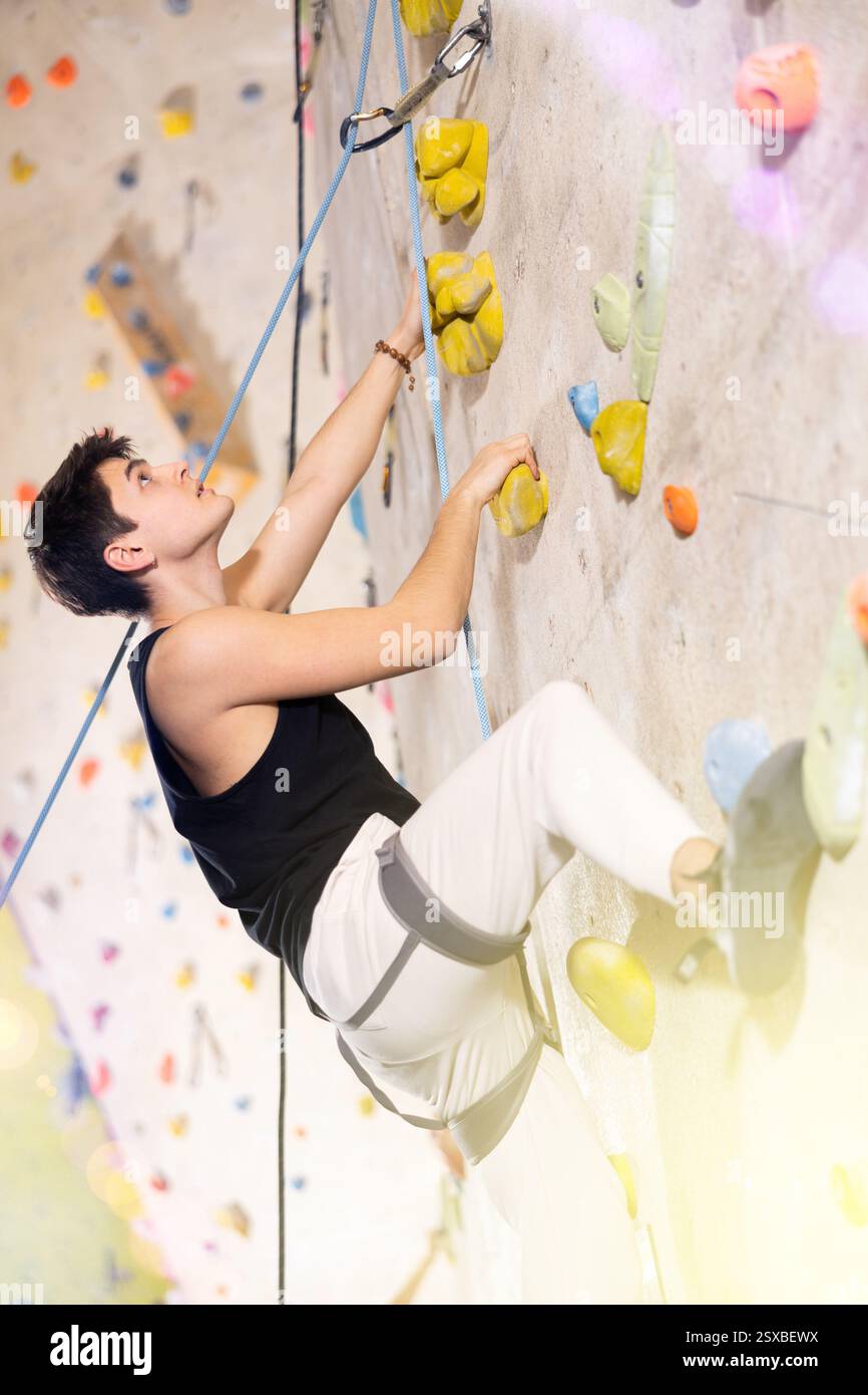 Side view of sportive young male climber moving up, using safety top ...