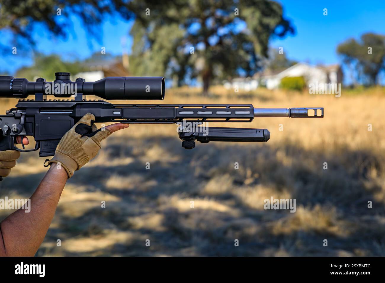 Male arm holding a modern precision rifle with a scope, aiming for a ...