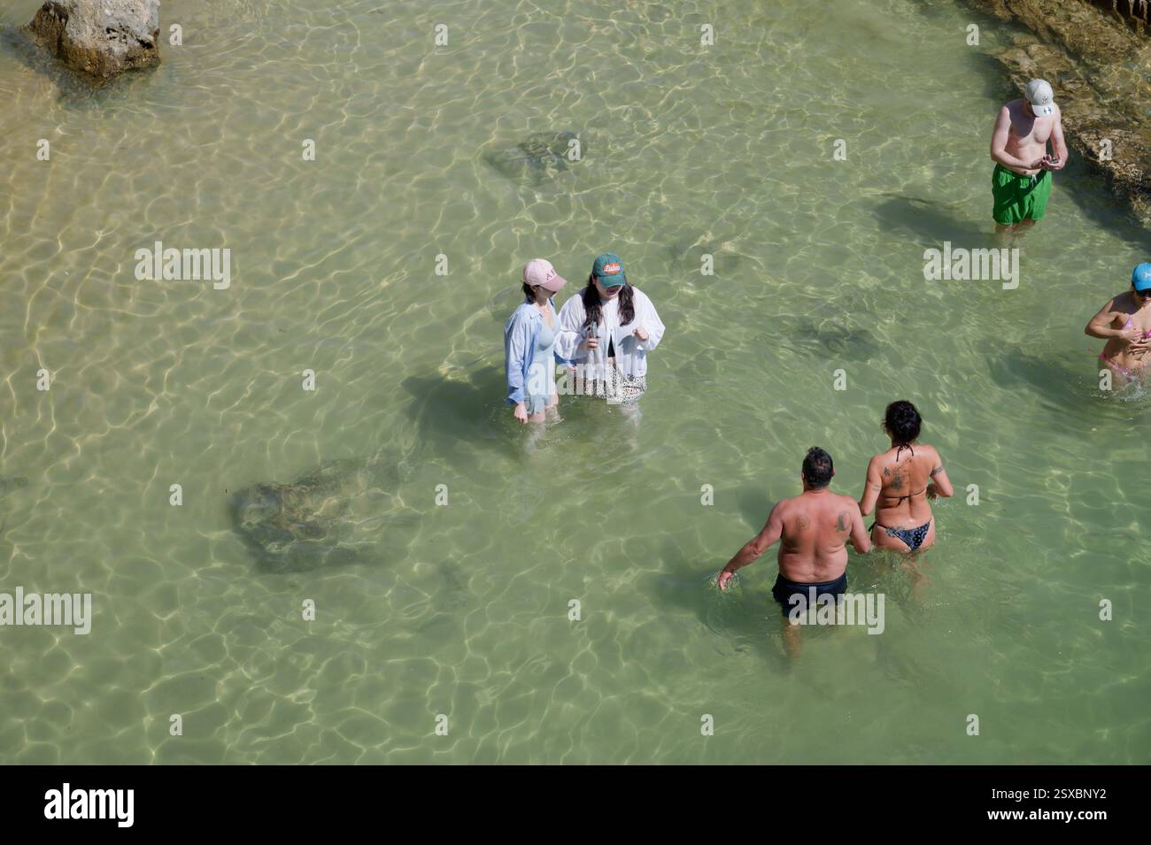 People wade through the shallow, sunlit waters of Santa Marta beach ...