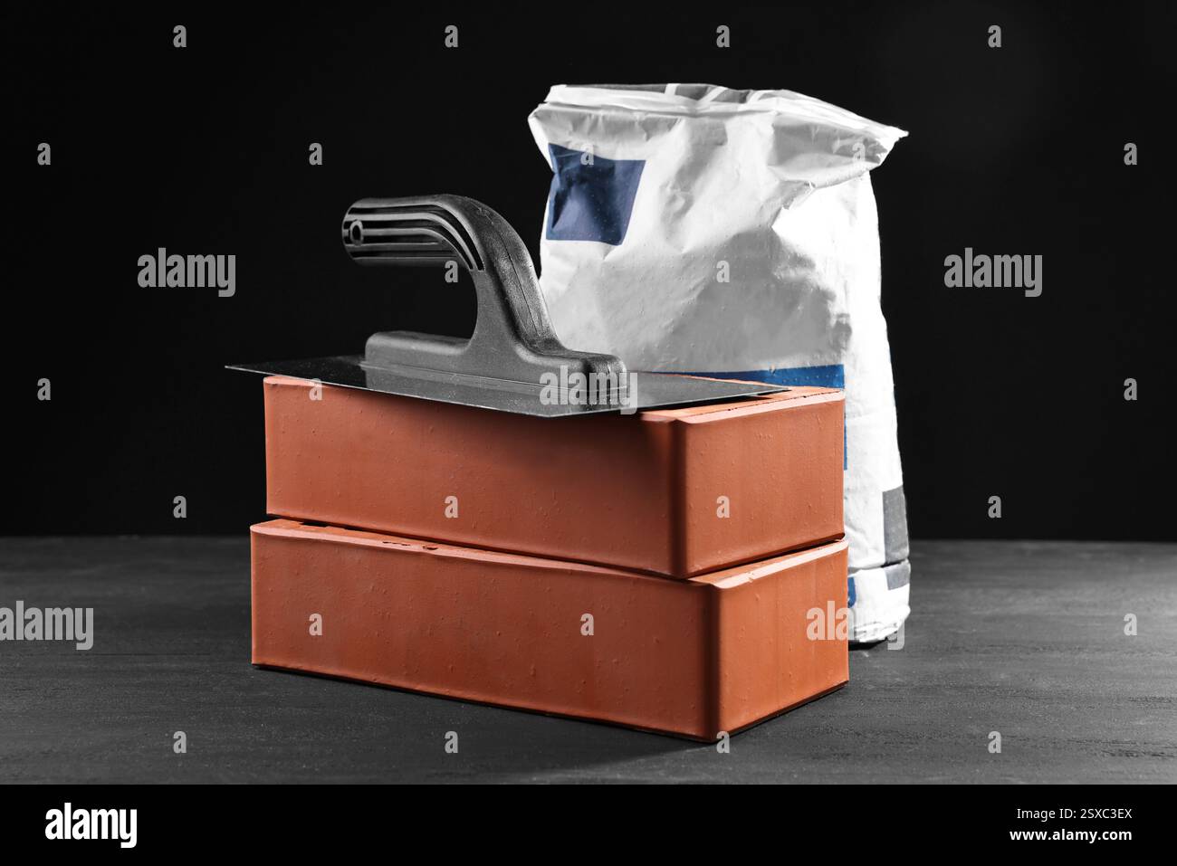 Bricks, bag of cement and construction tool on black table Stock Photo ...
