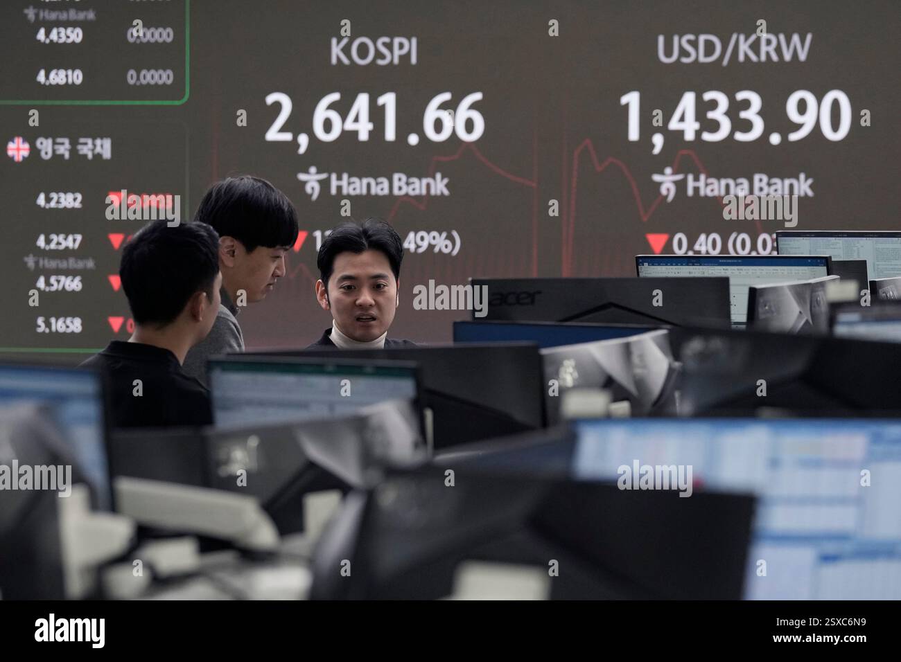 Currency traders watch monitors near a screen showing the Korea Composite Stock Price Index ...