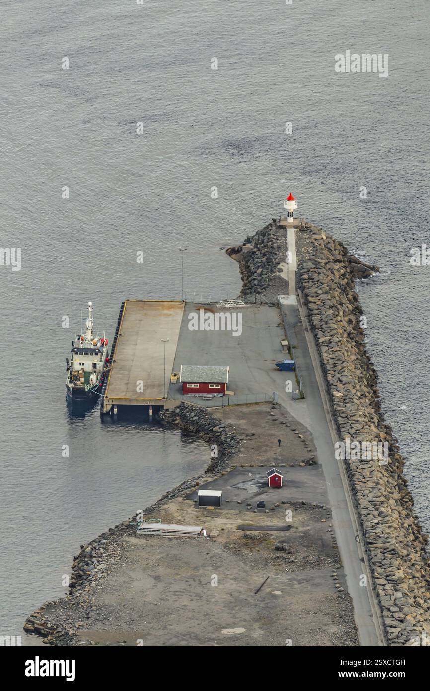 A ship docked at a pier with a lighthouse, set against a calm, rocky ...