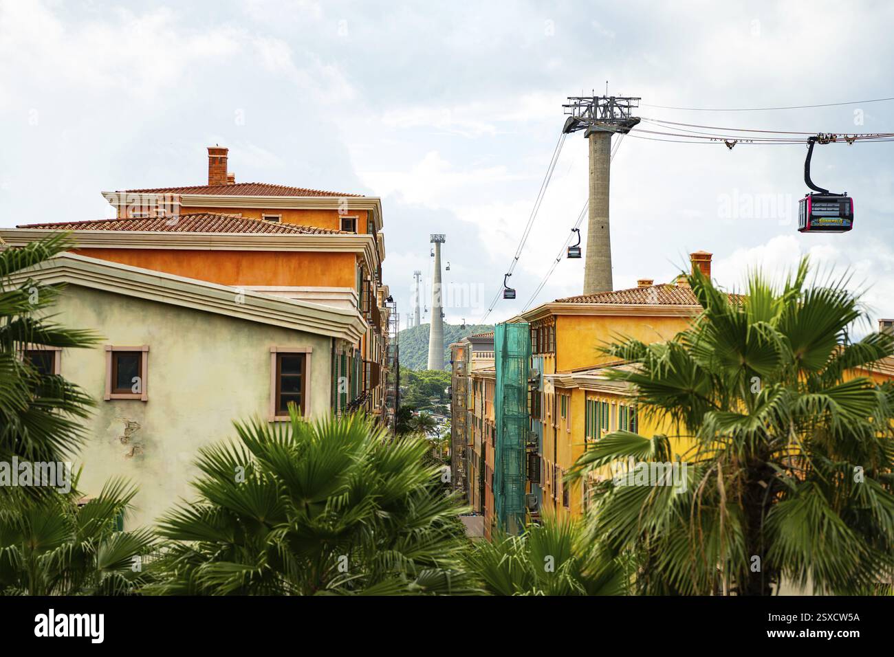 Cable car passing over colorful buildings with palm trees and an ...