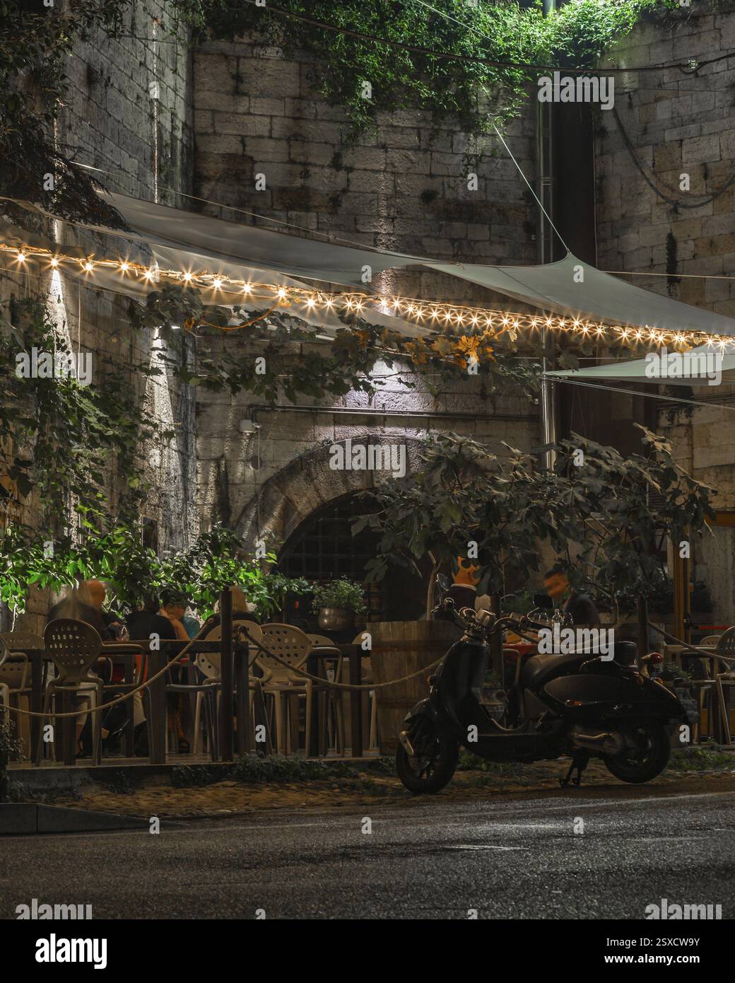Cozy outdoor seating under vines and string lights near a brick wall ...