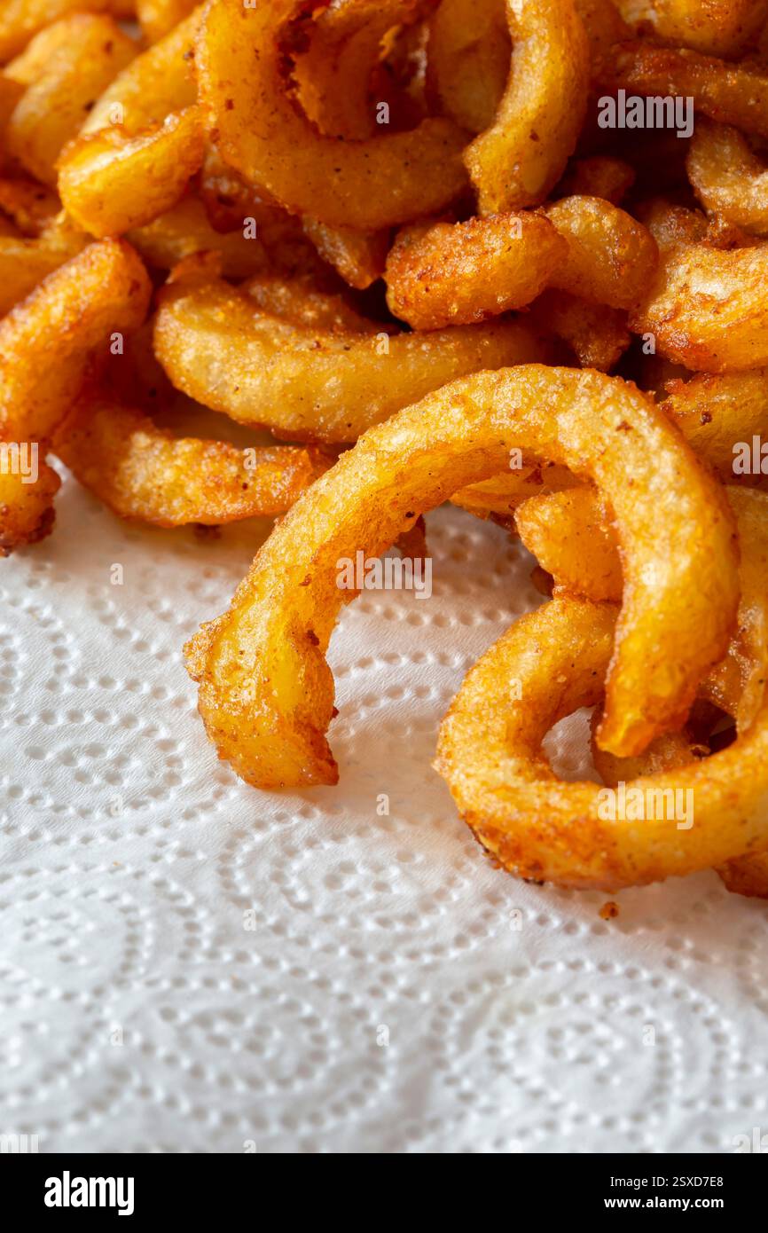 Seasoned spicy curly fries, freshly fried, on kitchen paper towel ...