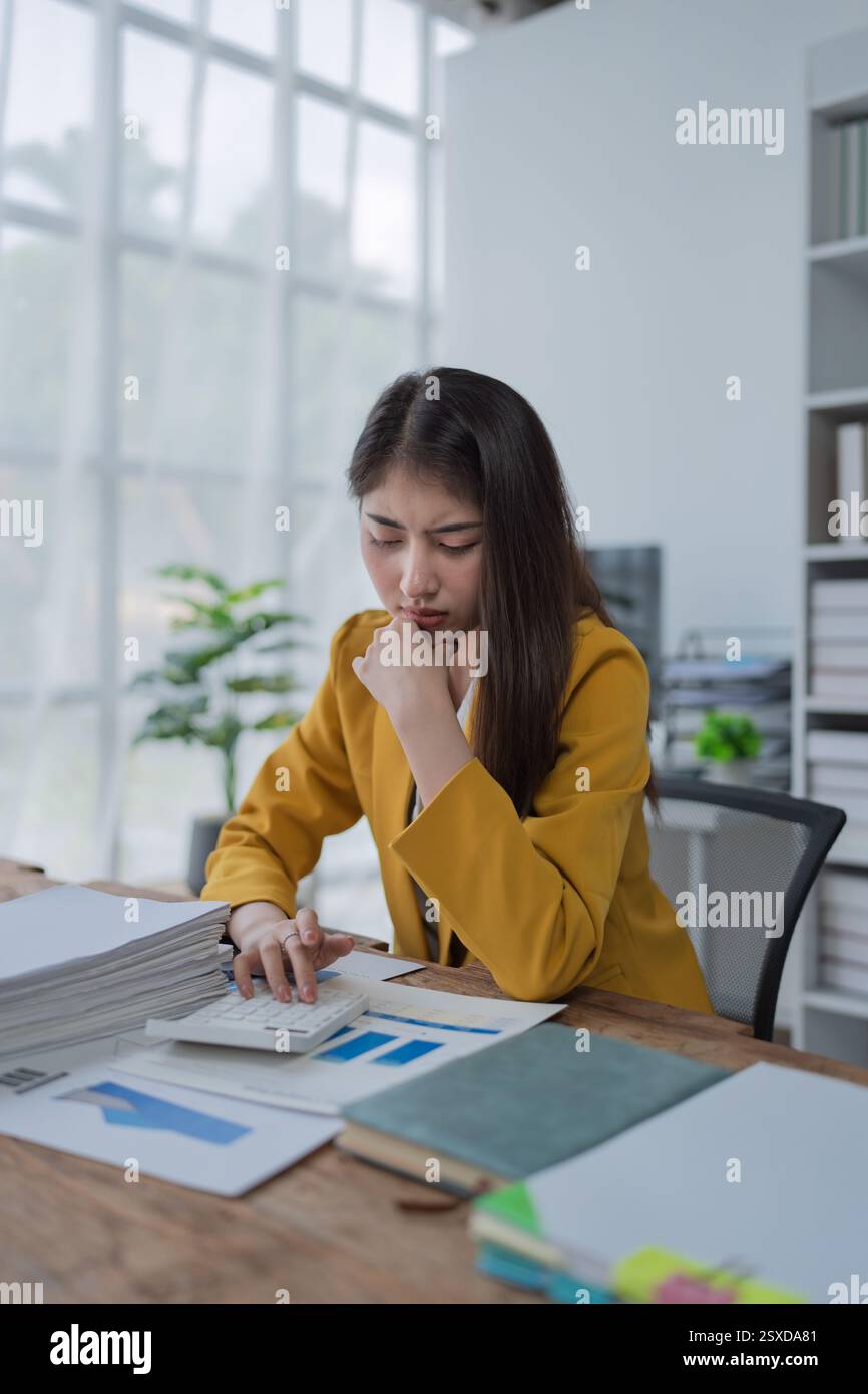 Young businesswoman analyzing reports and charts in a modern office environment while working on ...