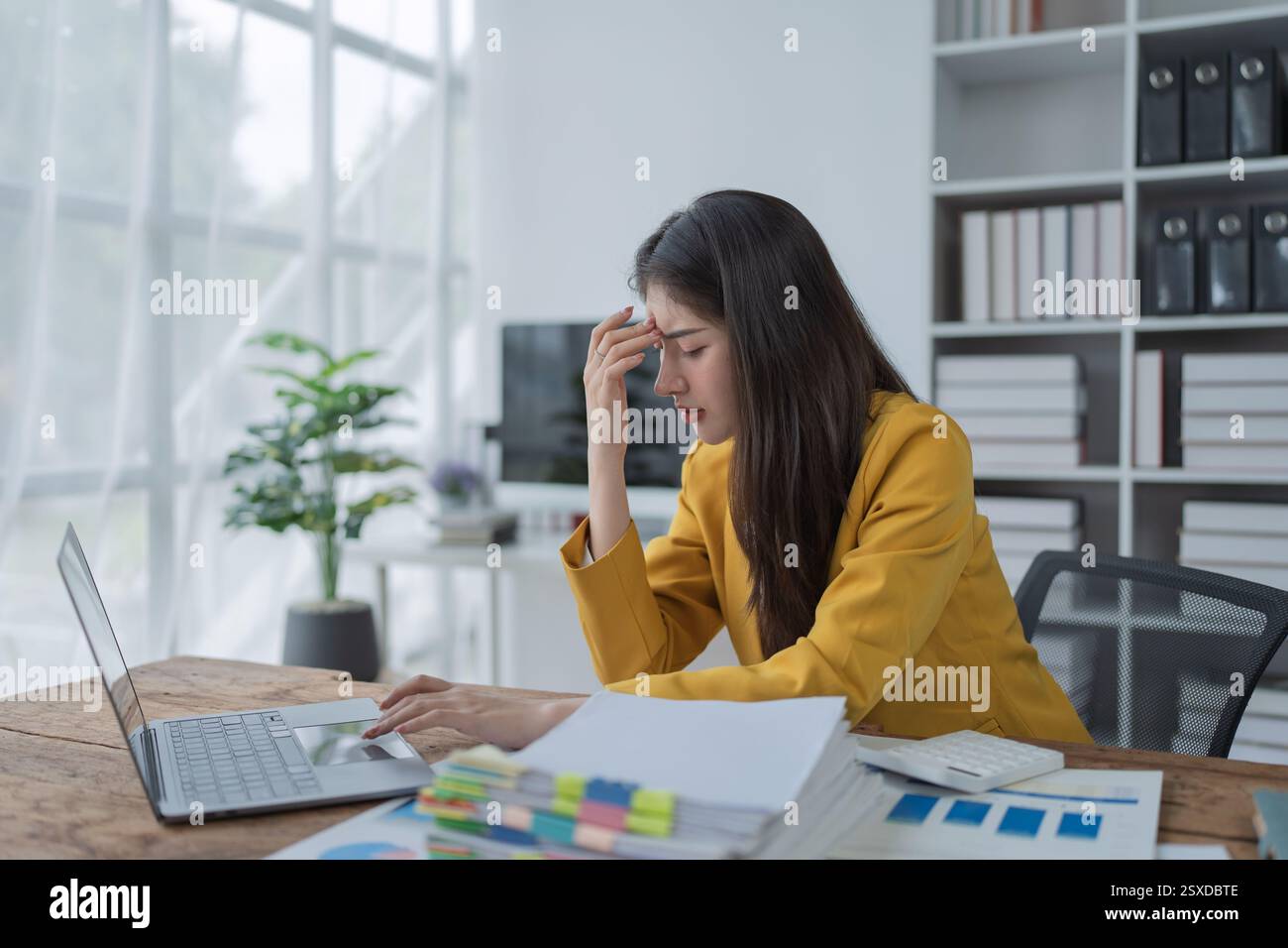 Overwhelmed businesswoman experiencing stress while working on a laptop in a modern office ...