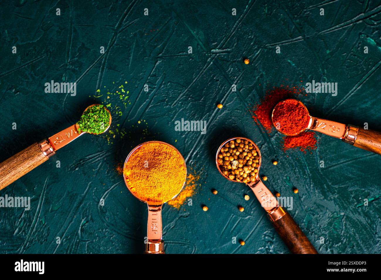 Spices in copper measuring spoons on a malachite textured background ...