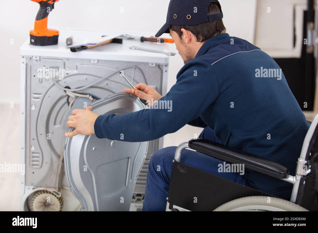serviceman in wheelchair repairs a washing machine Stock Photo - Alamy