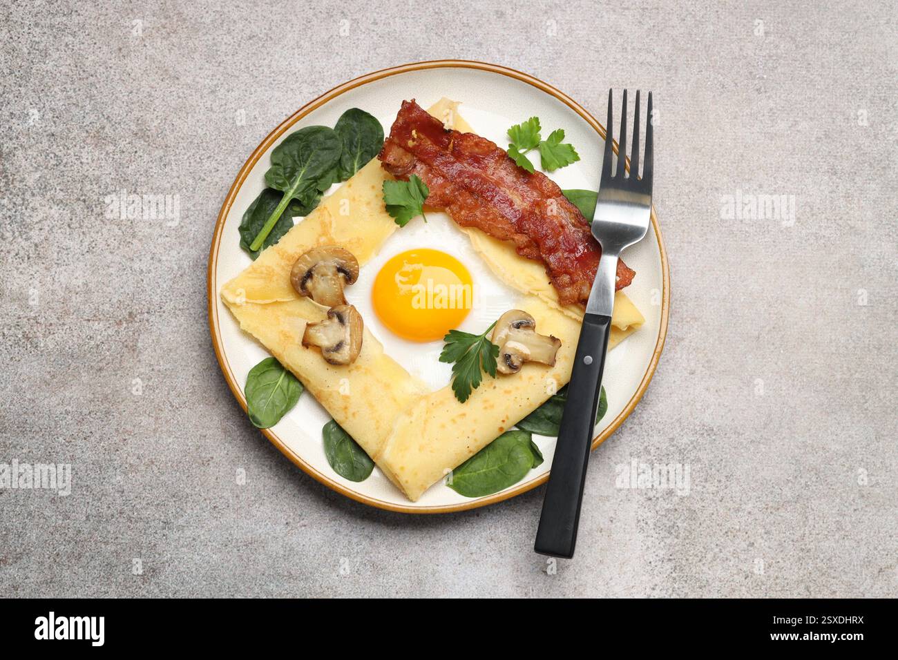 Delicious crepe with egg, bacon and mushrooms served on grey table, top ...