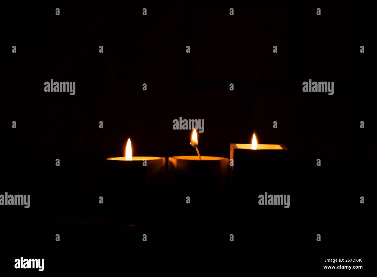 Three homemade candles in plaster candlesticks burn in the dark of the ...