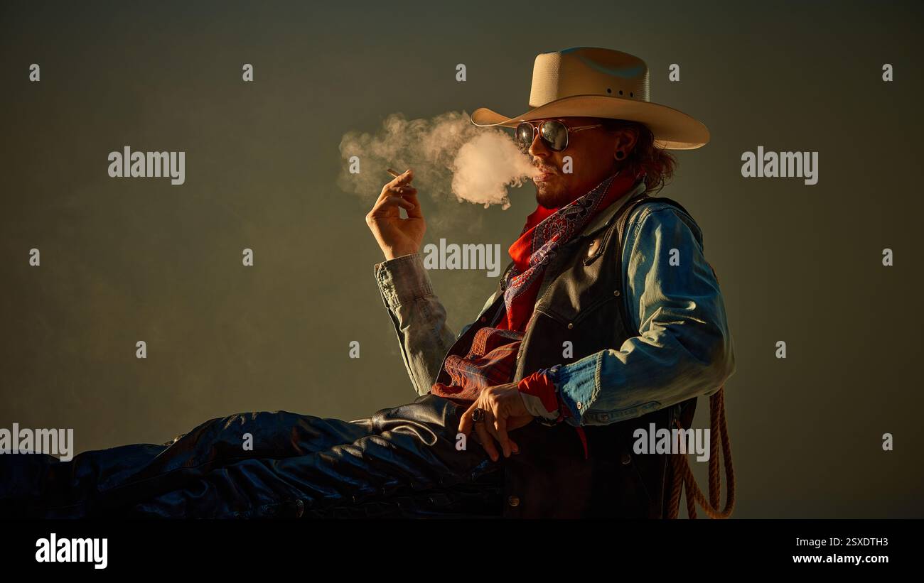 Man dressed as cowboy lounging in leather pants, denim jacket, smoking ...