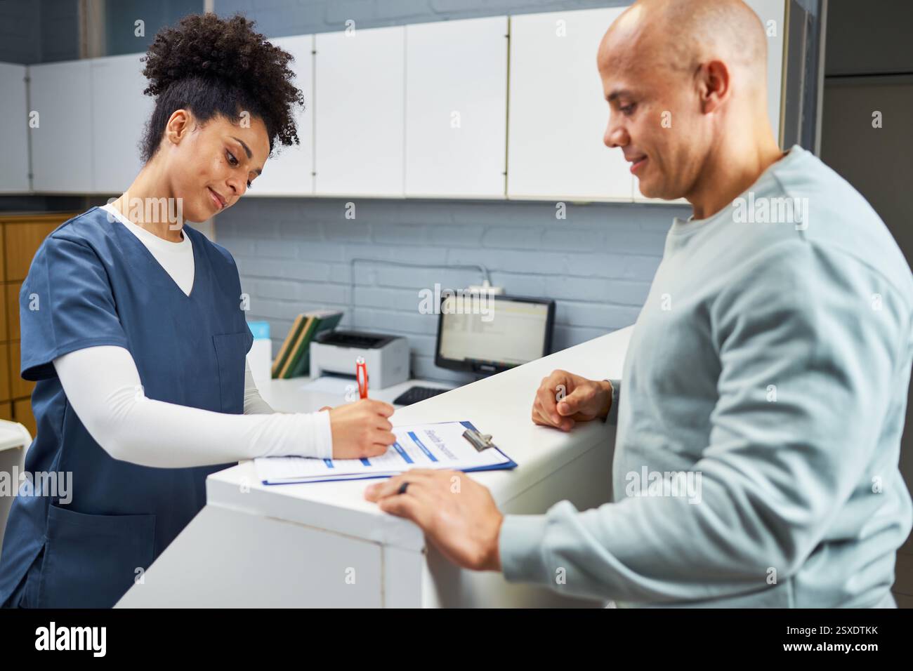 Healthcare Worker Assisting Patient at Reception Desk with Forms in ...