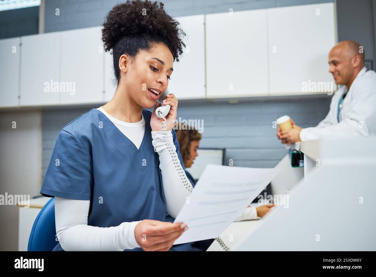 Healthcare Professional Talking on Phone in Reception Area with a Team ...