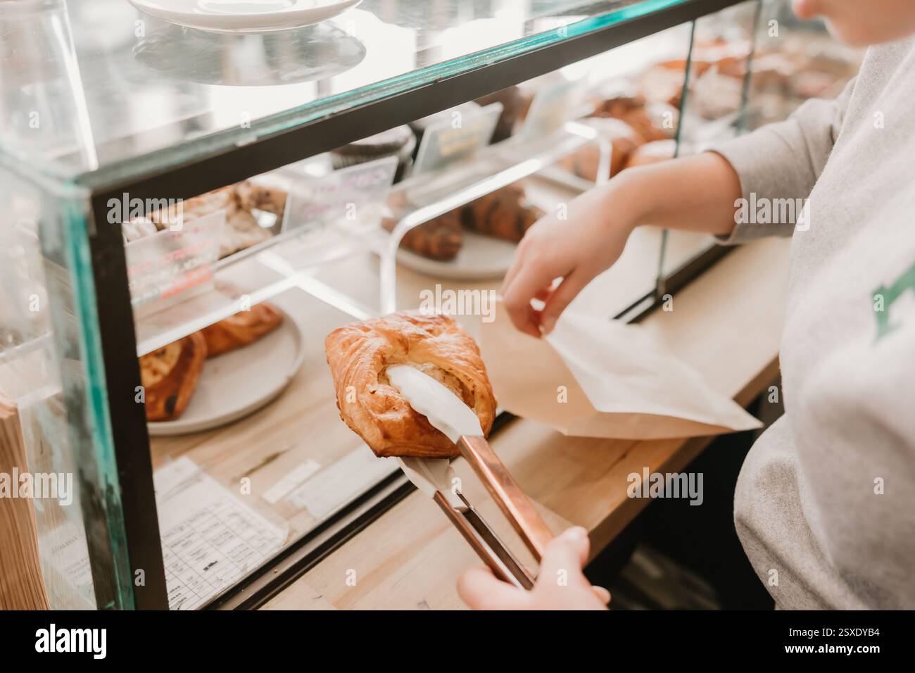 Barista using tongs to place a pastry into a bag at cafe counter Stock ...