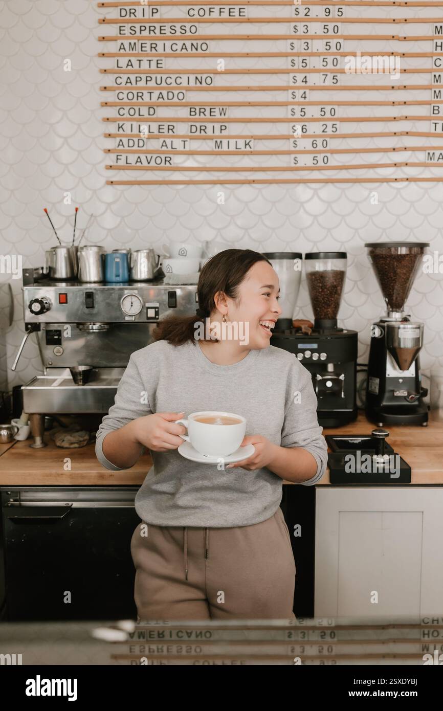 Smiling barista holding latte in a modern coffee shop with menu board ...
