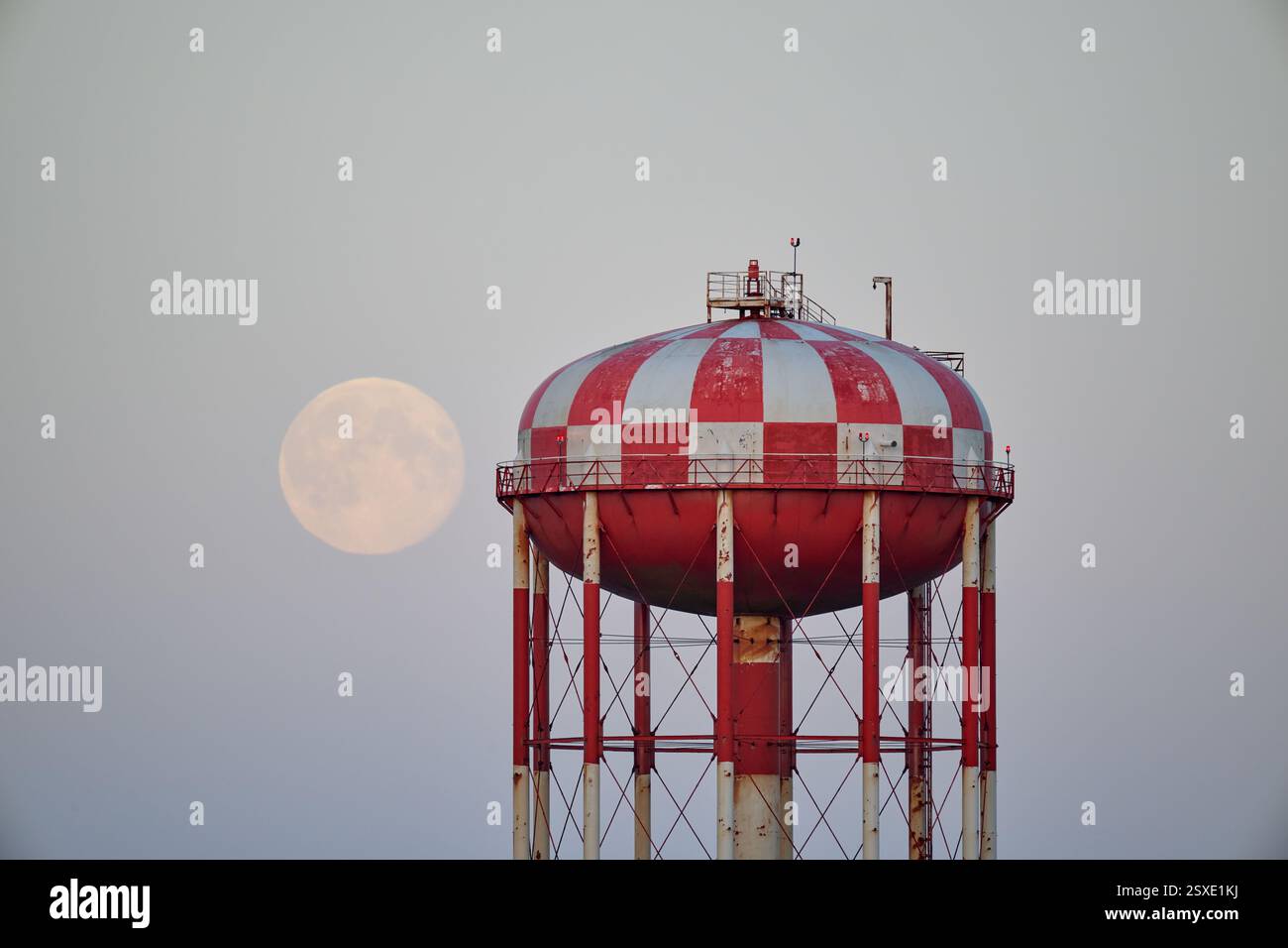 Large moon rising next to checkered water tower Stock Photo - Alamy