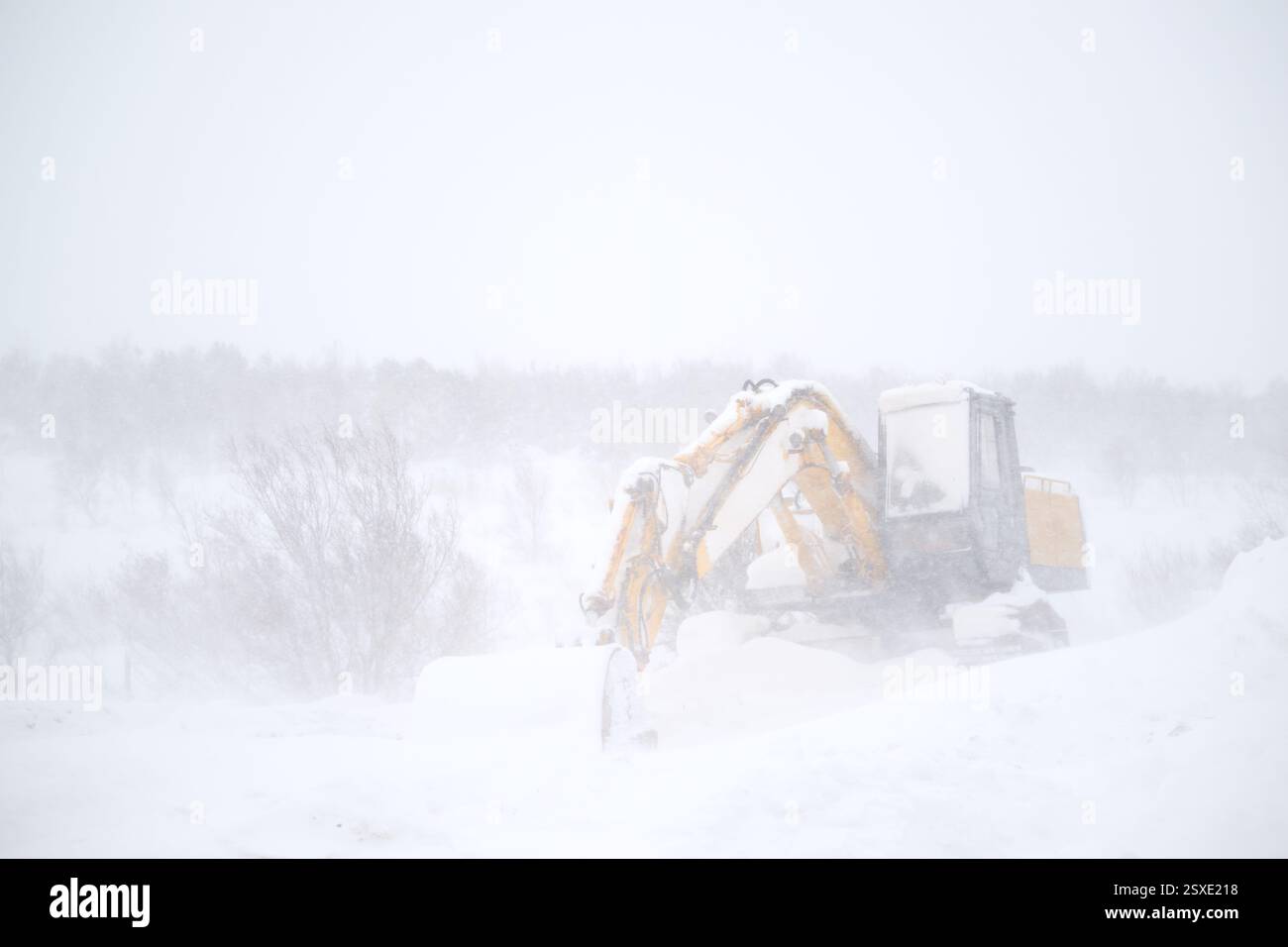 Excavator covered in snow during heavy snowfall in winter landscape ...