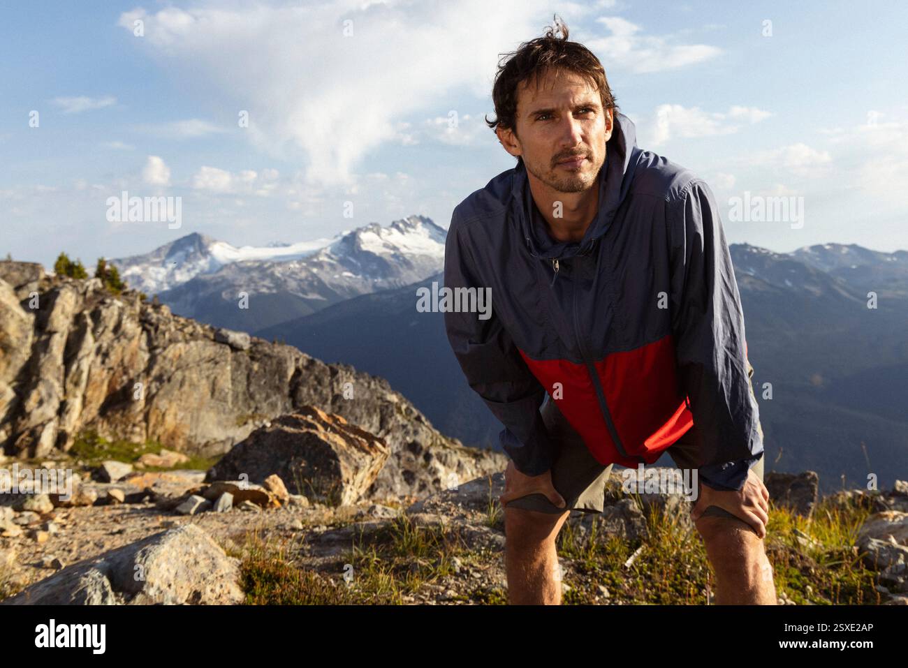 Trail runner on mountain catching breath with rugged peaks behind Stock ...