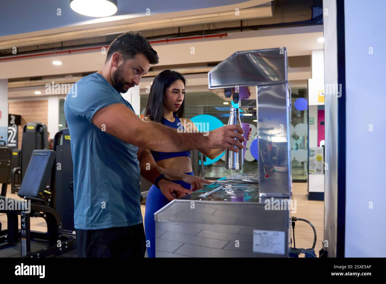 Two fitness enthusiasts refilling their water bottles at a gym ...