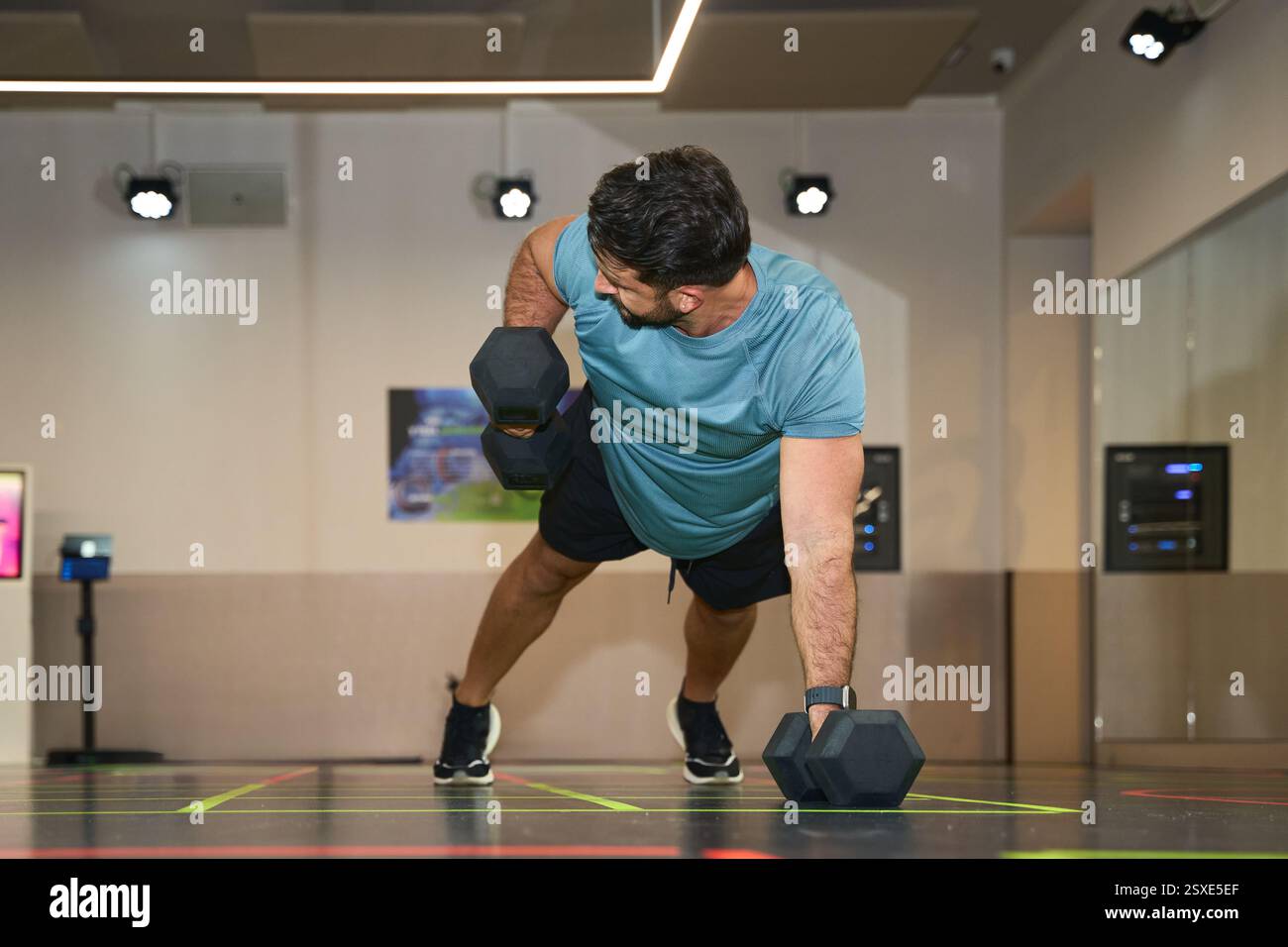 Athletic man engaging in a dynamic dumbbell workout on a gym floor ...