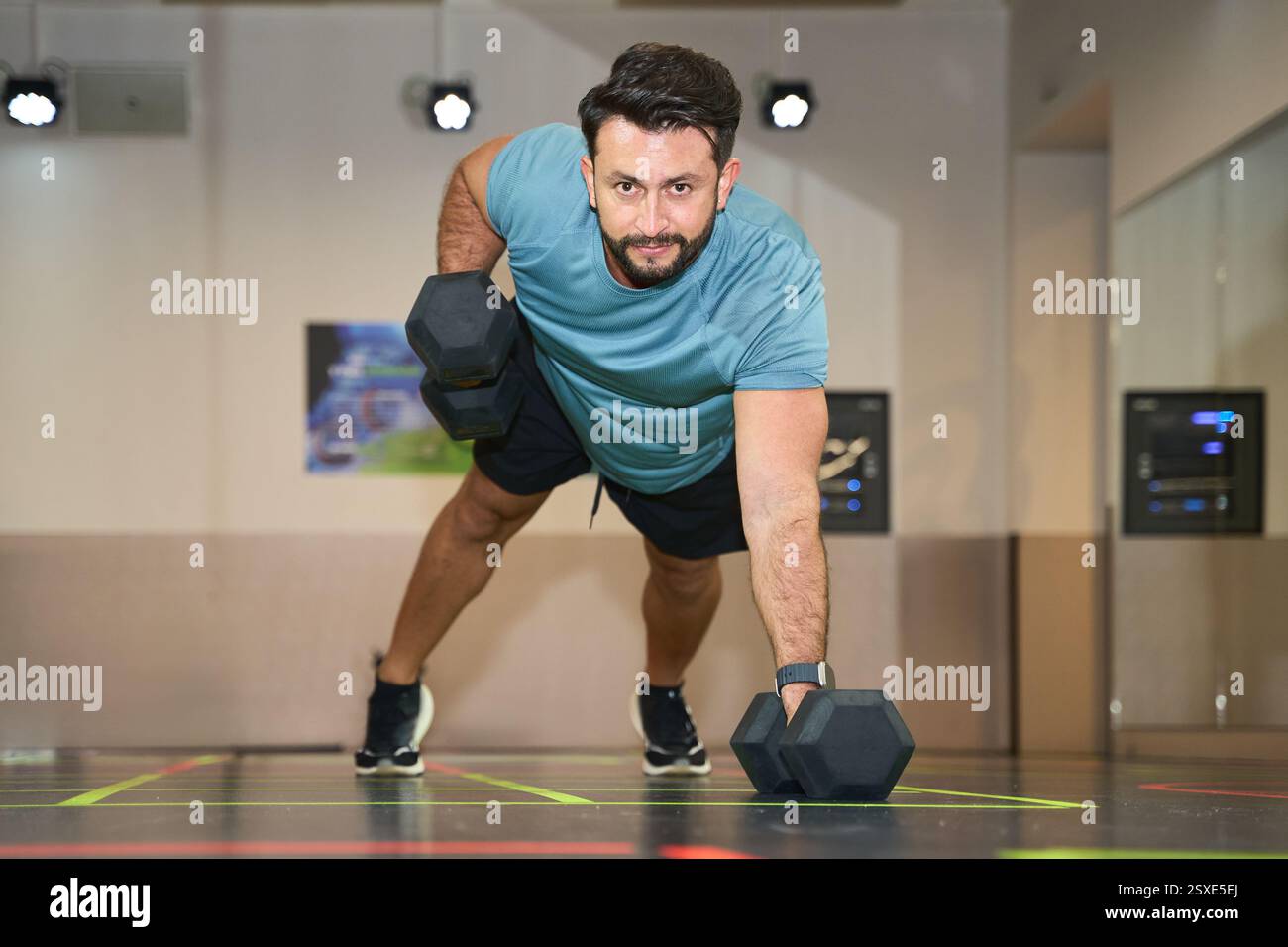 Athletic man performing a plank row with dumbbells in a gym ...