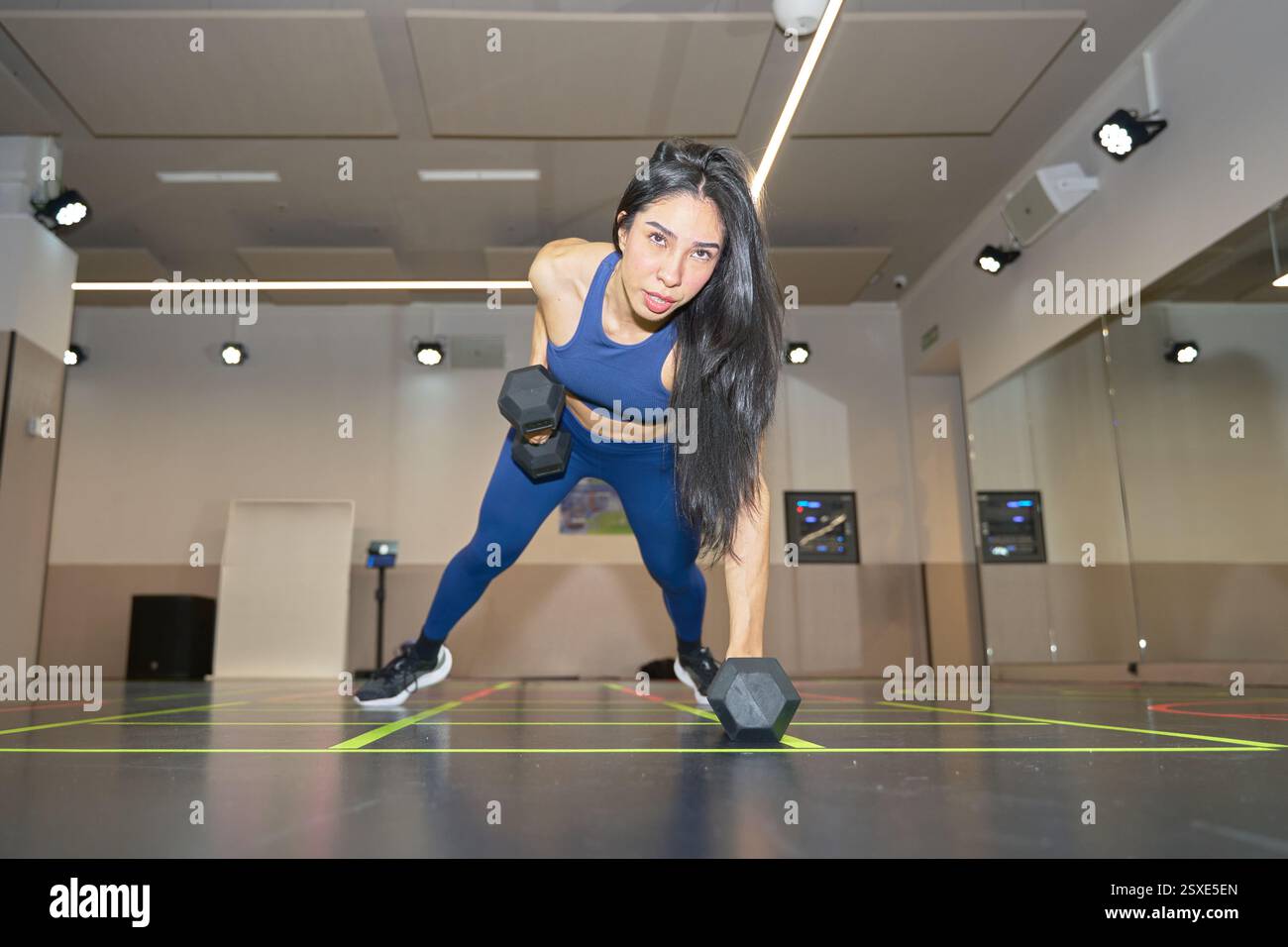 Focused woman executing a dynamic dumbbell exercise on a marked gym ...