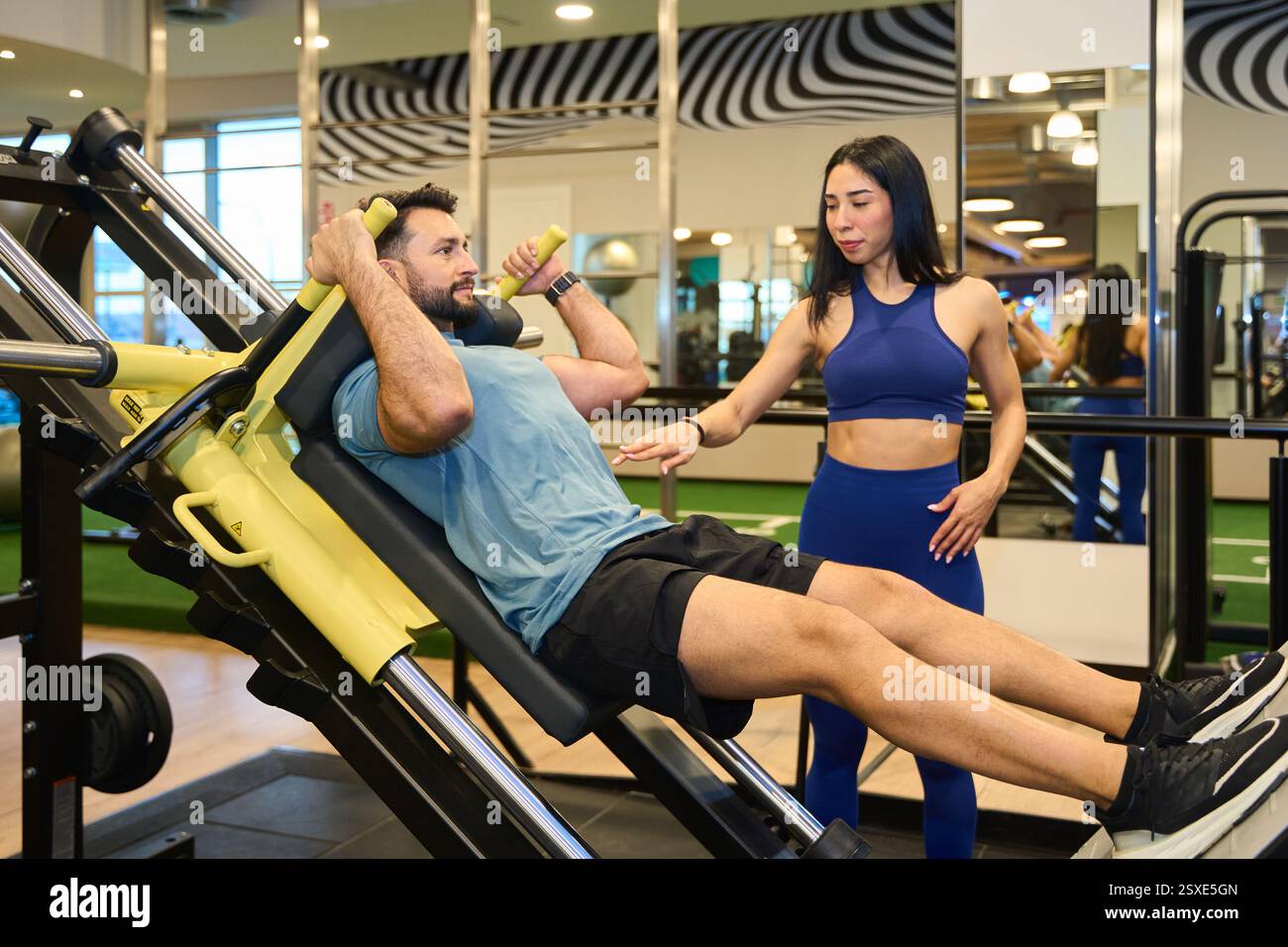 Fitness trainer guiding a client through a leg press workout in a ...