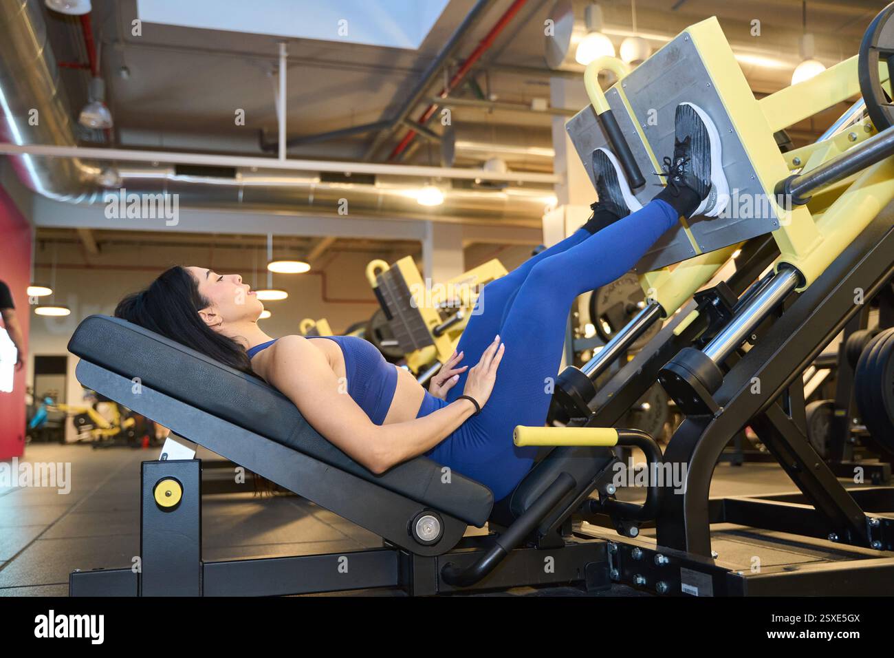 Woman in athletic wear using a leg press machine at a modern gym ...