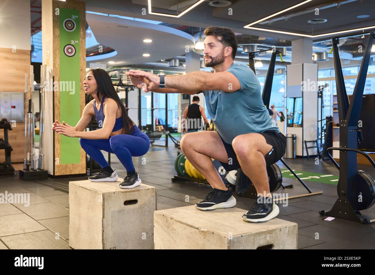 Two fitness enthusiasts performing box squats on wooden platforms at a ...