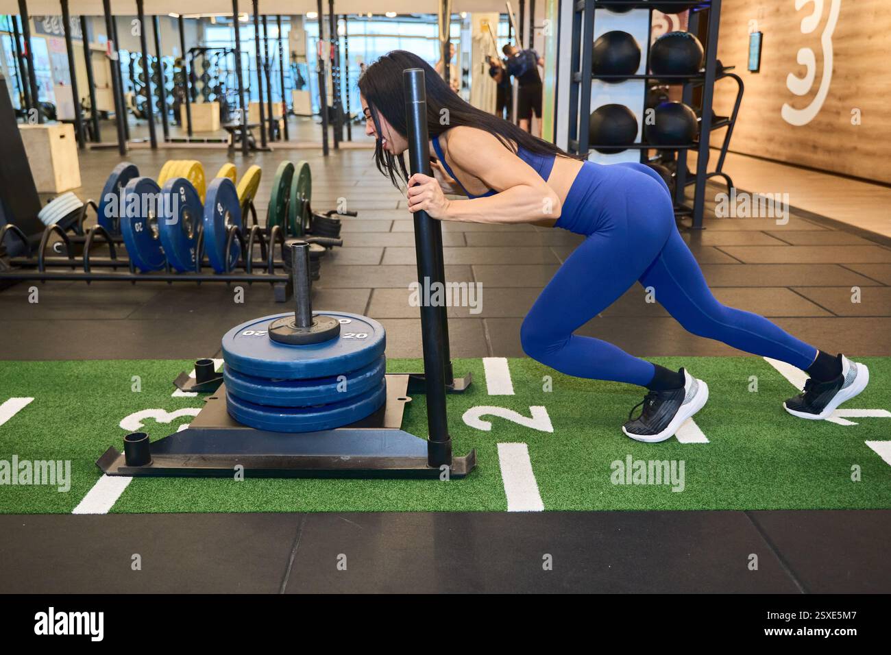 Woman pushing a weighted sled on a green turf in a modern gym ...