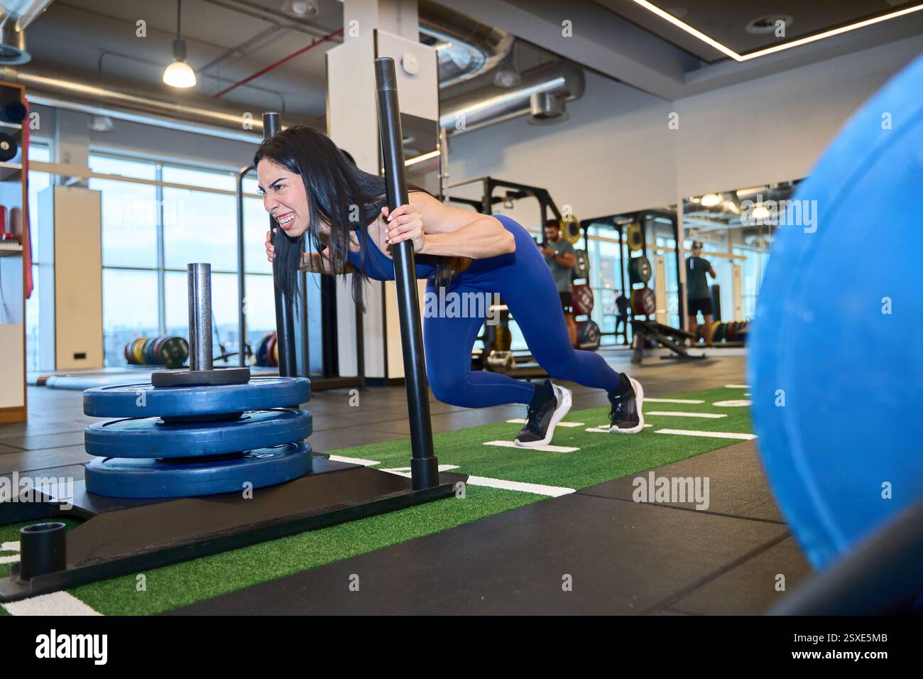 Focused athlete pushing a weighted sled on turf in a modern gym ...