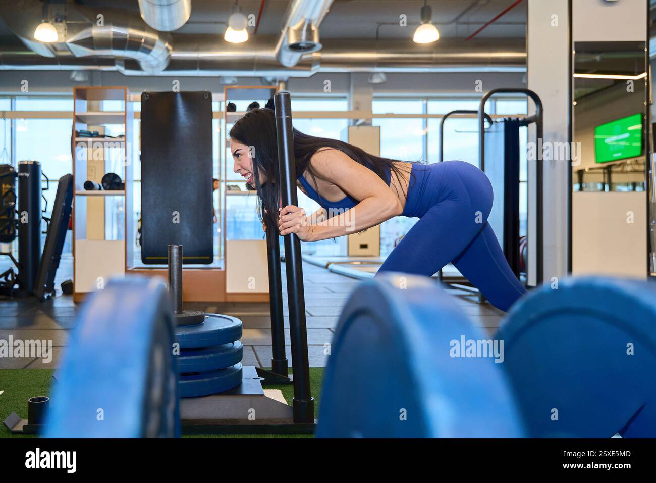 Focused woman in a gym performing a sled push exercise, showcasing ...