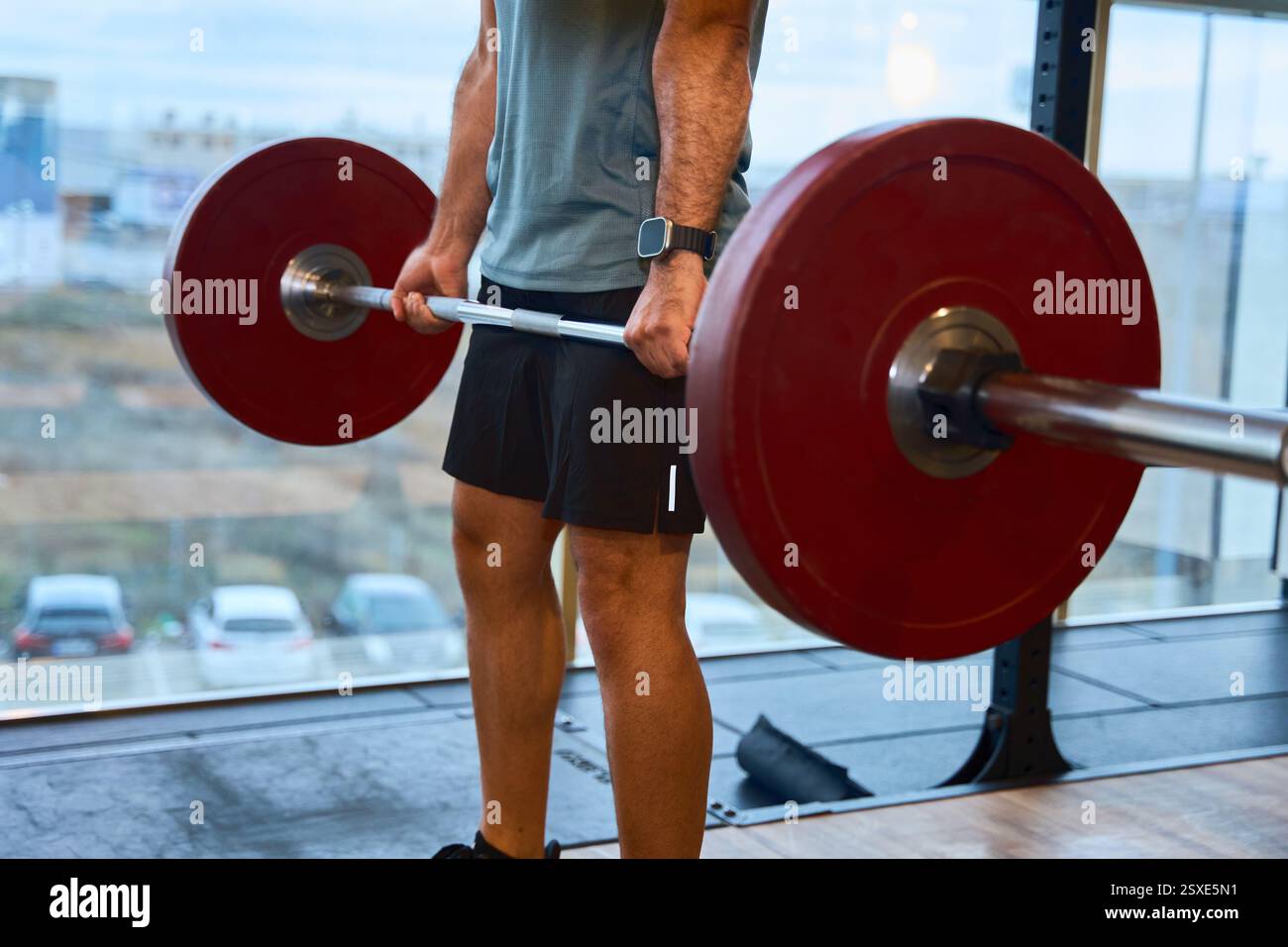 Focused athlete lifting heavy barbell in a gym with large windows ...