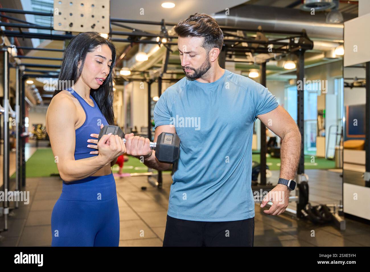 Personal trainer guides a woman in proper dumbbell lifting technique at ...