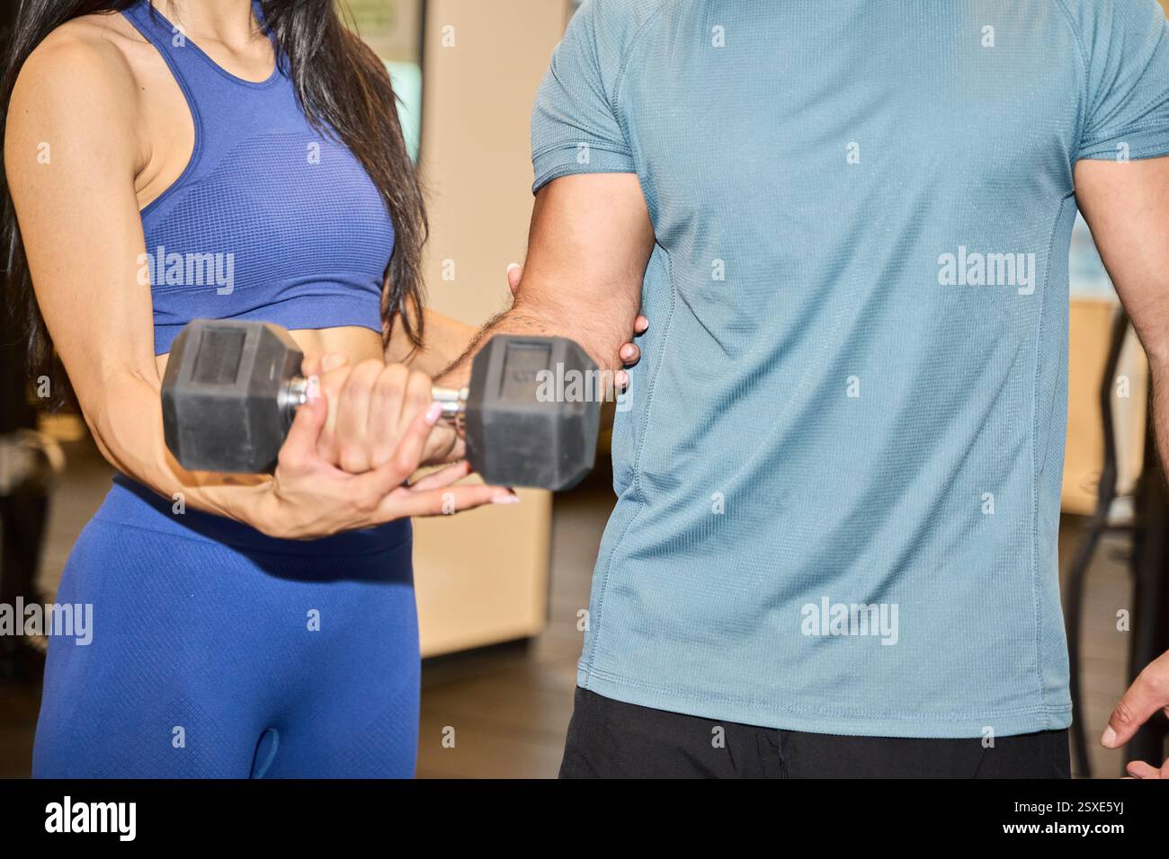 Personal trainer guides client in proper dumbbell technique at the gym, focusing on strength ...