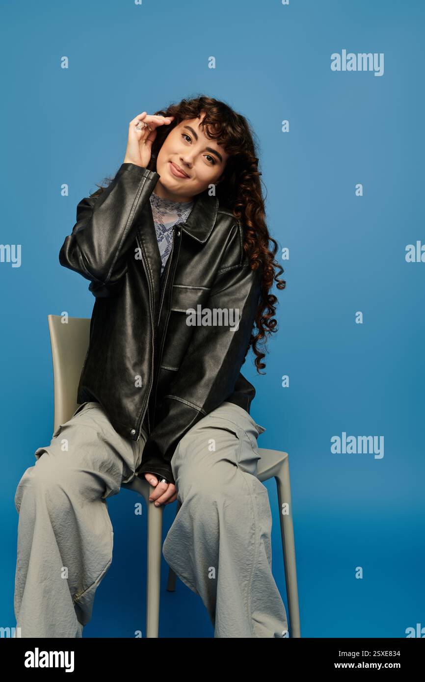 A trendy young woman with curly hair poses in front of a vibrant blue ...