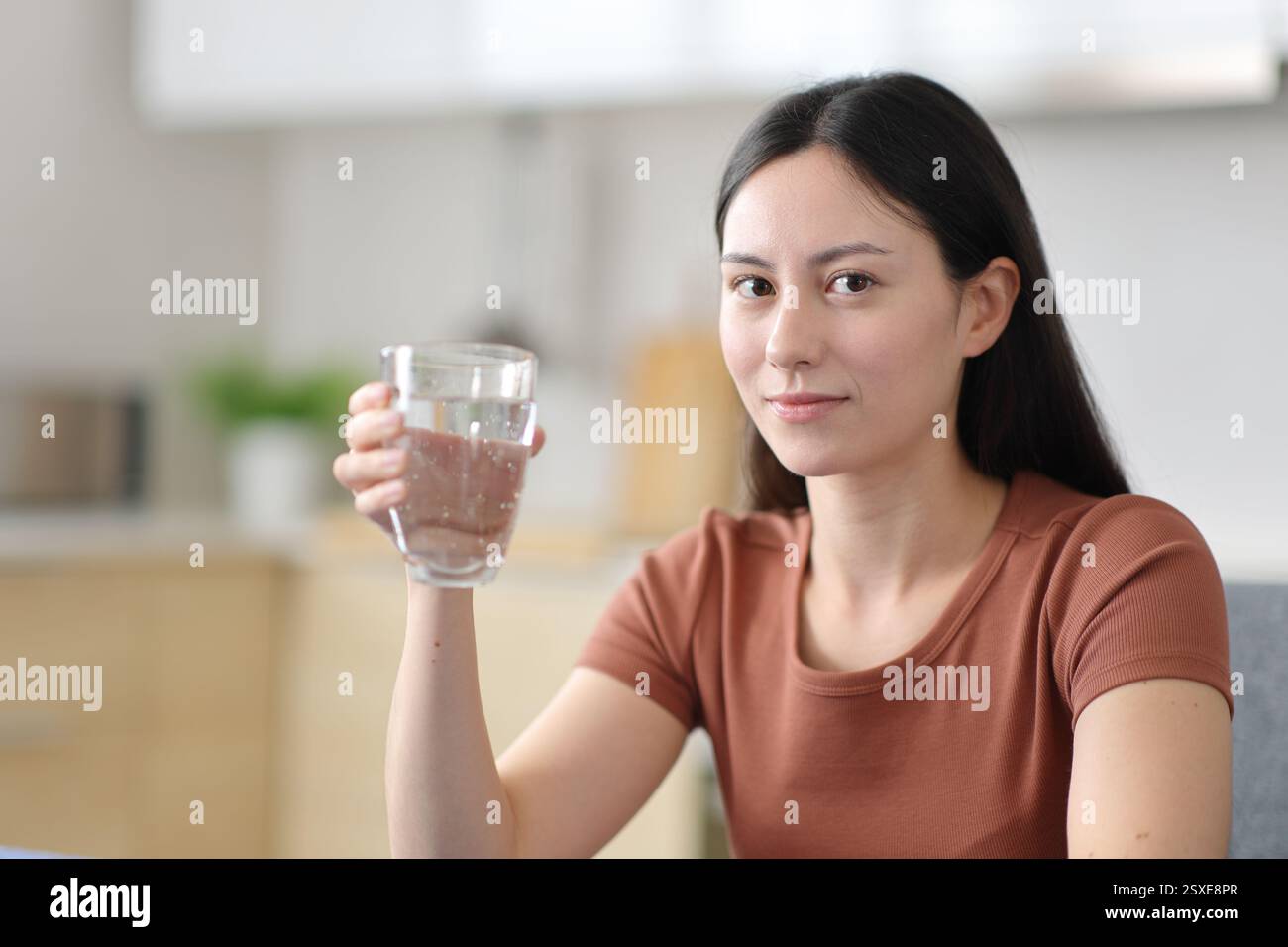 Serious asian woman holding glass of water in the kitchen at home Stock ...