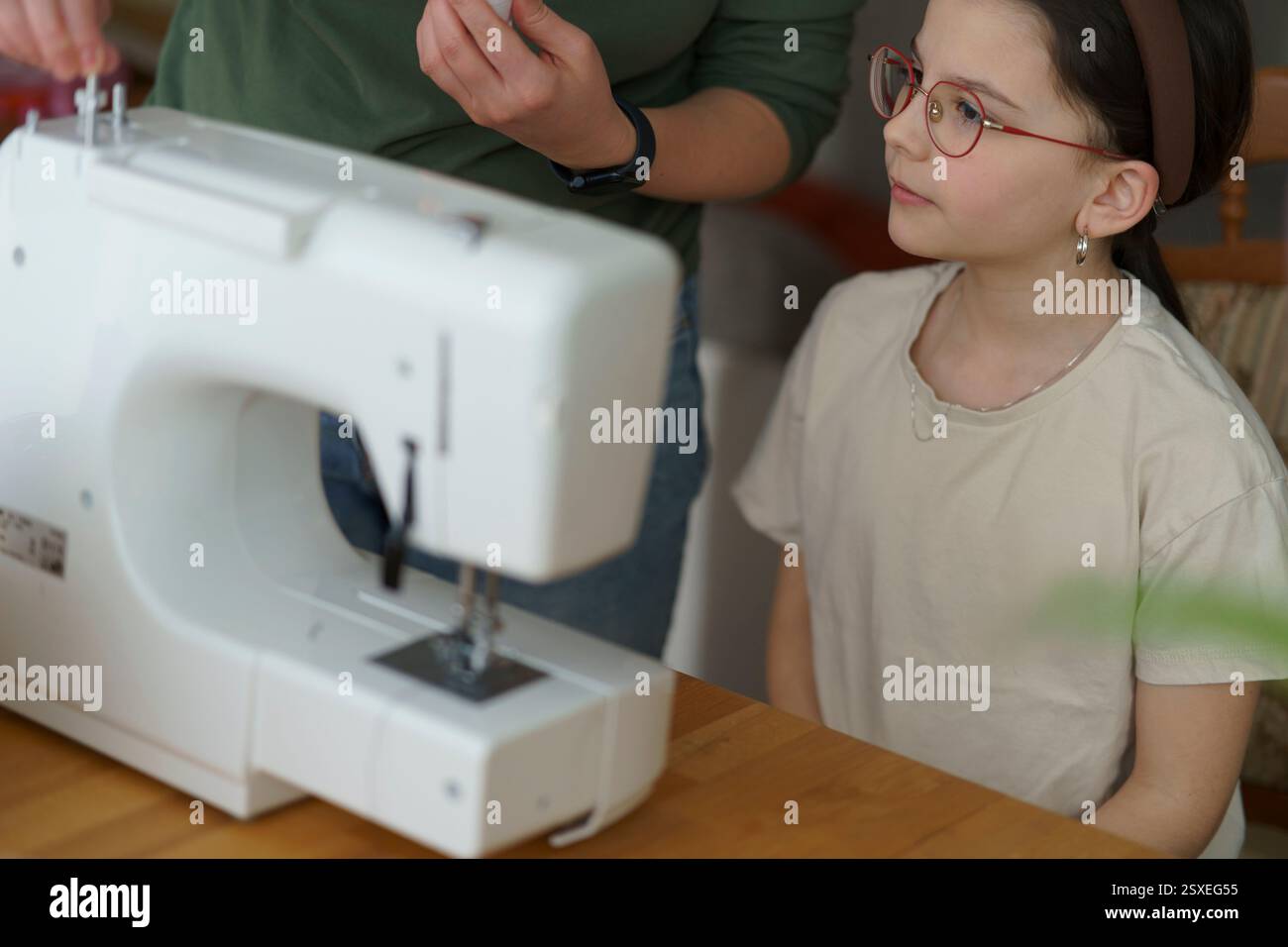 A mother shows her daughter how to thread a sewing machine and sew ...