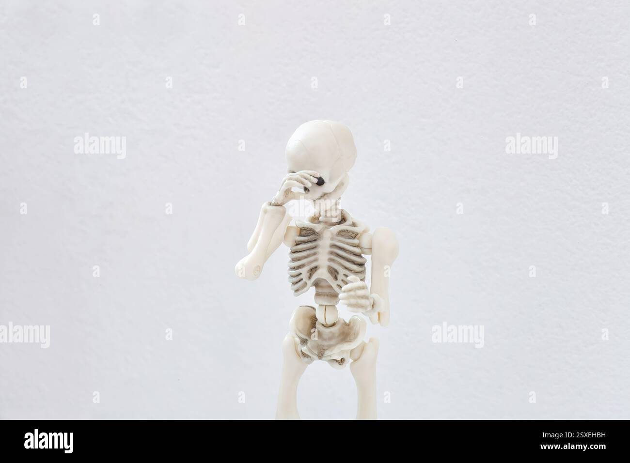 Human skeleton covers his face with his hand by white wall background ...