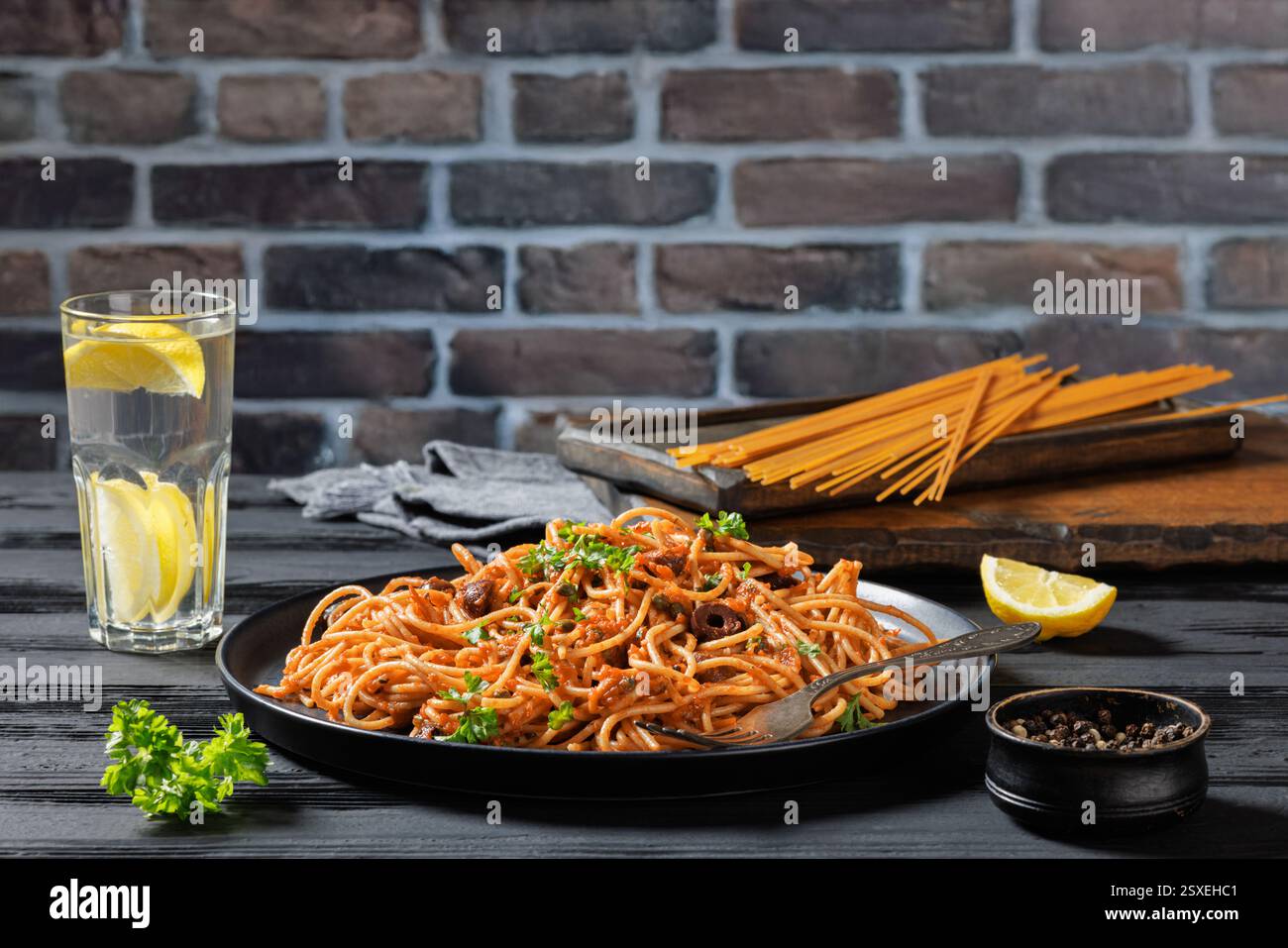 vegan whole grain spaghetti alla puttanesca on a plate on black wooden ...