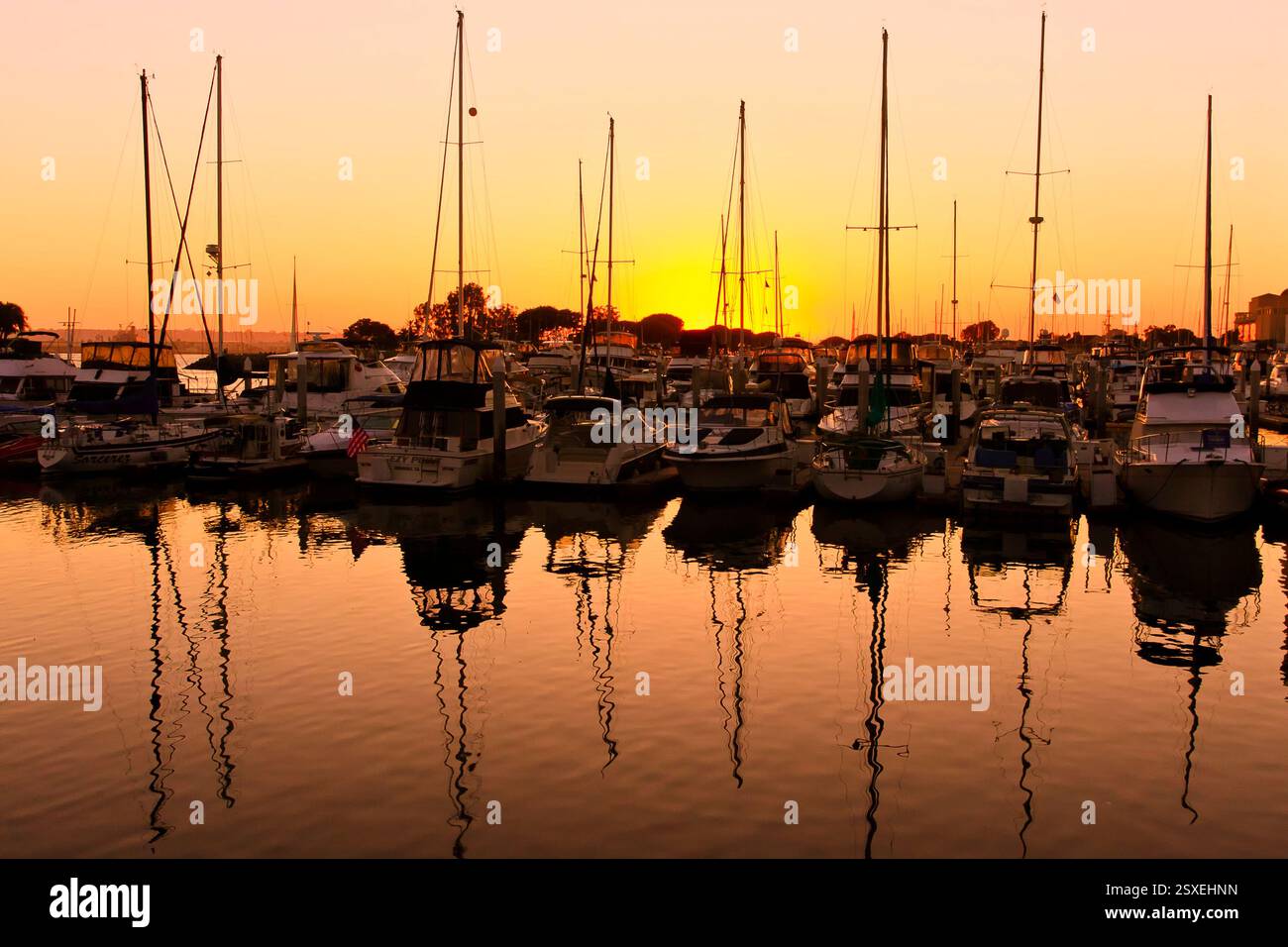 Group of boats are parked at a marina, with the sun setting in the ...