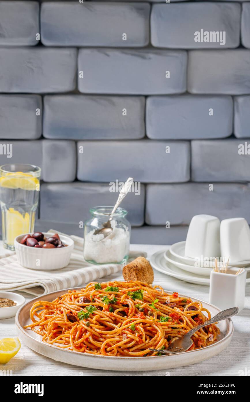 vegan whole grain spaghetti alla puttanesca on a plate on white wooden ...