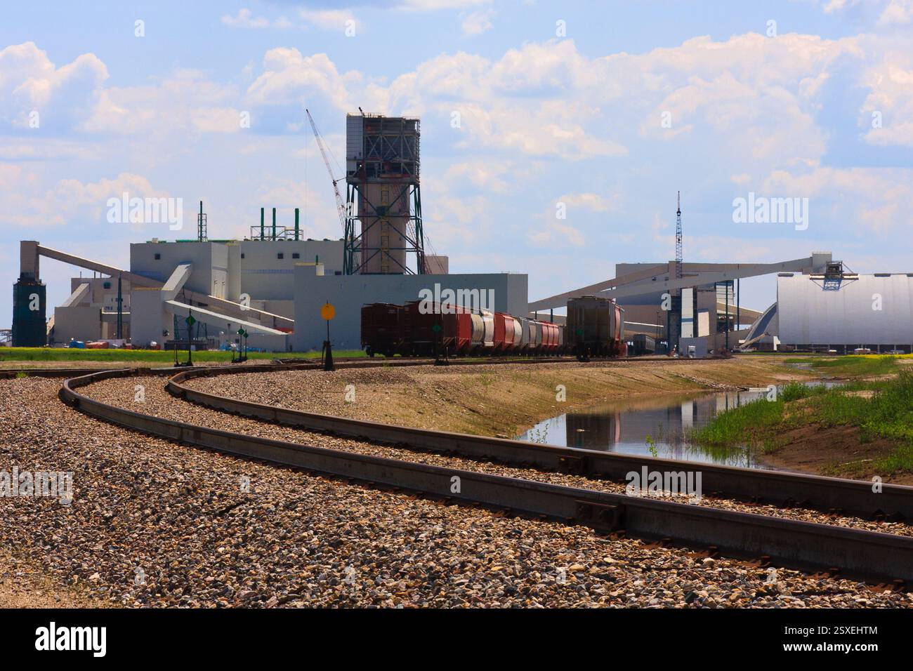 Train is traveling down a track next to a large industrial plant. The ...