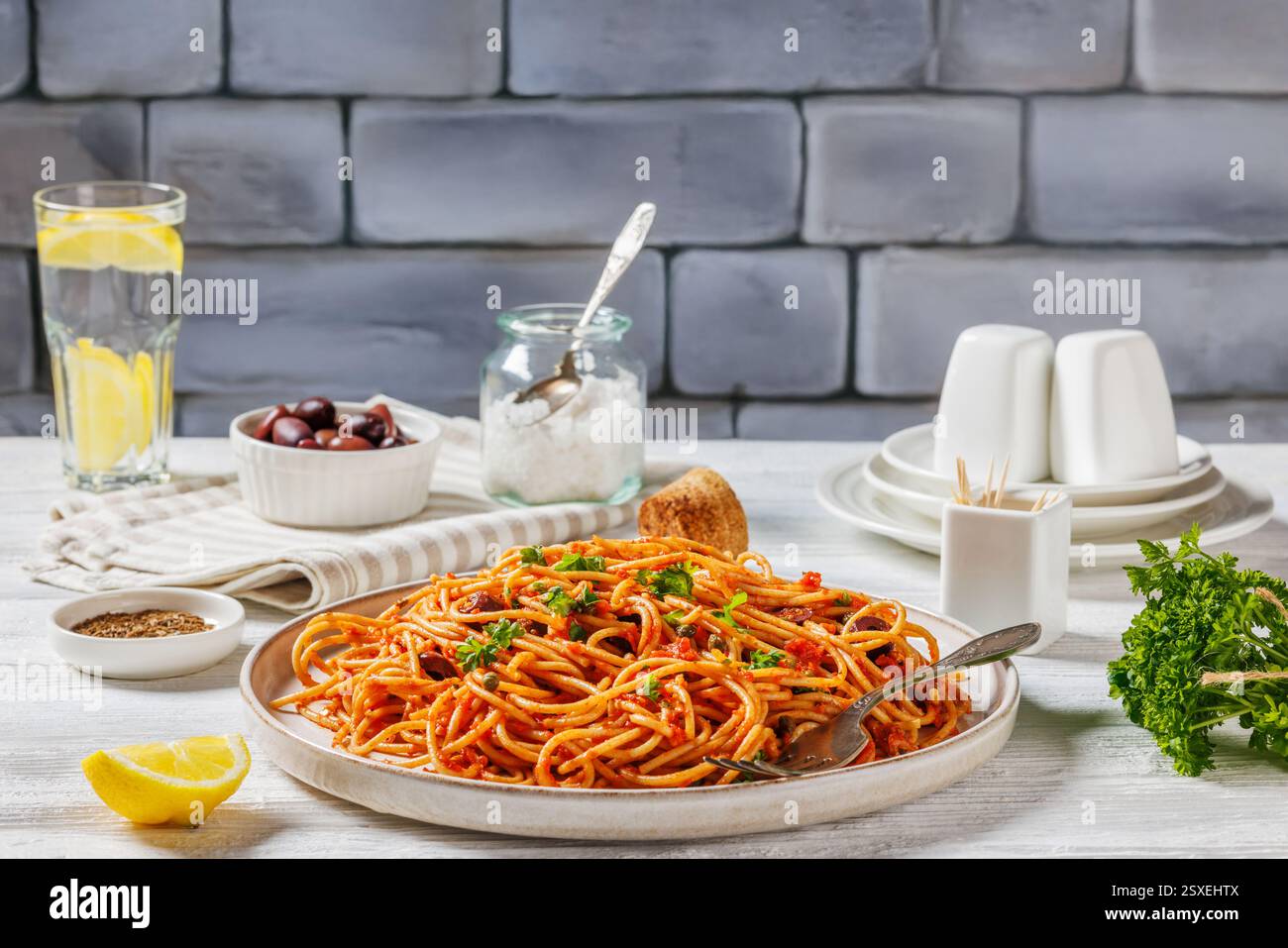 vegan whole grain spaghetti alla puttanesca on a plate on white wooden ...