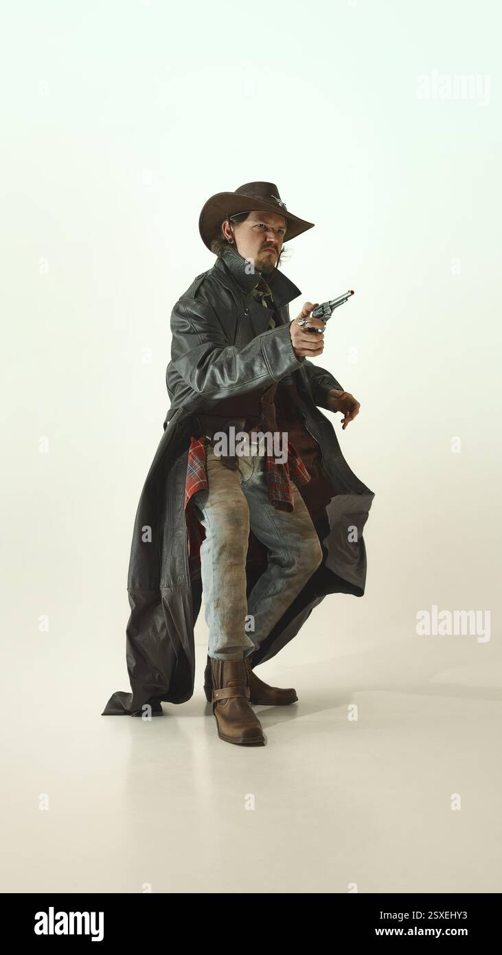 Portrait of man, cowboy aiming revolver, wearing rugged leather trench ...