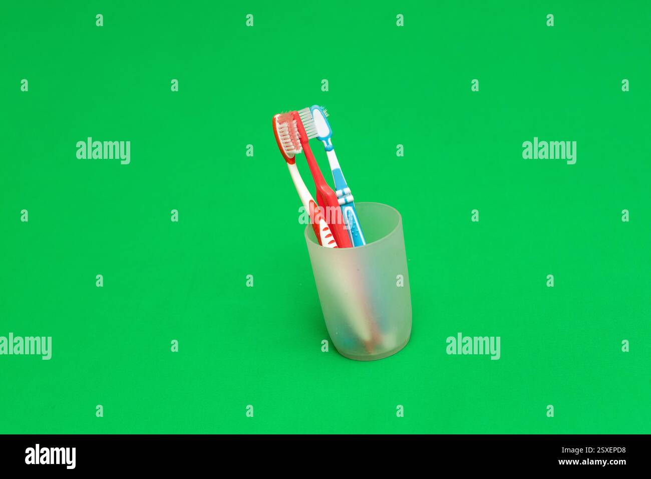 Two colorful toothbrushes are standing in a translucent plastic cup ...